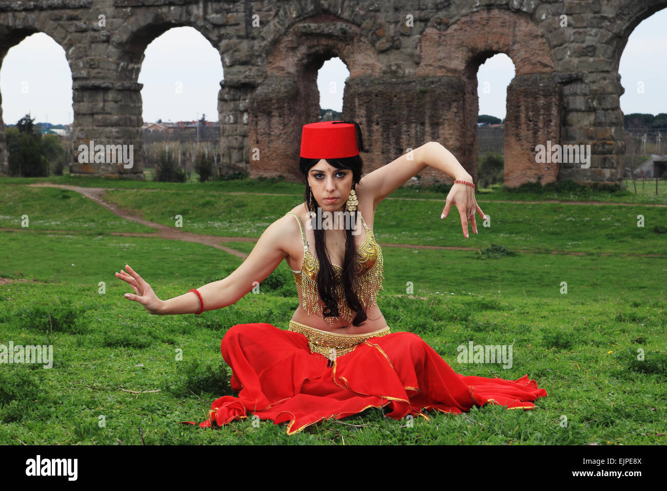 red hat belly dancer sitting in front of Roman aqueduct ruins Stock ...