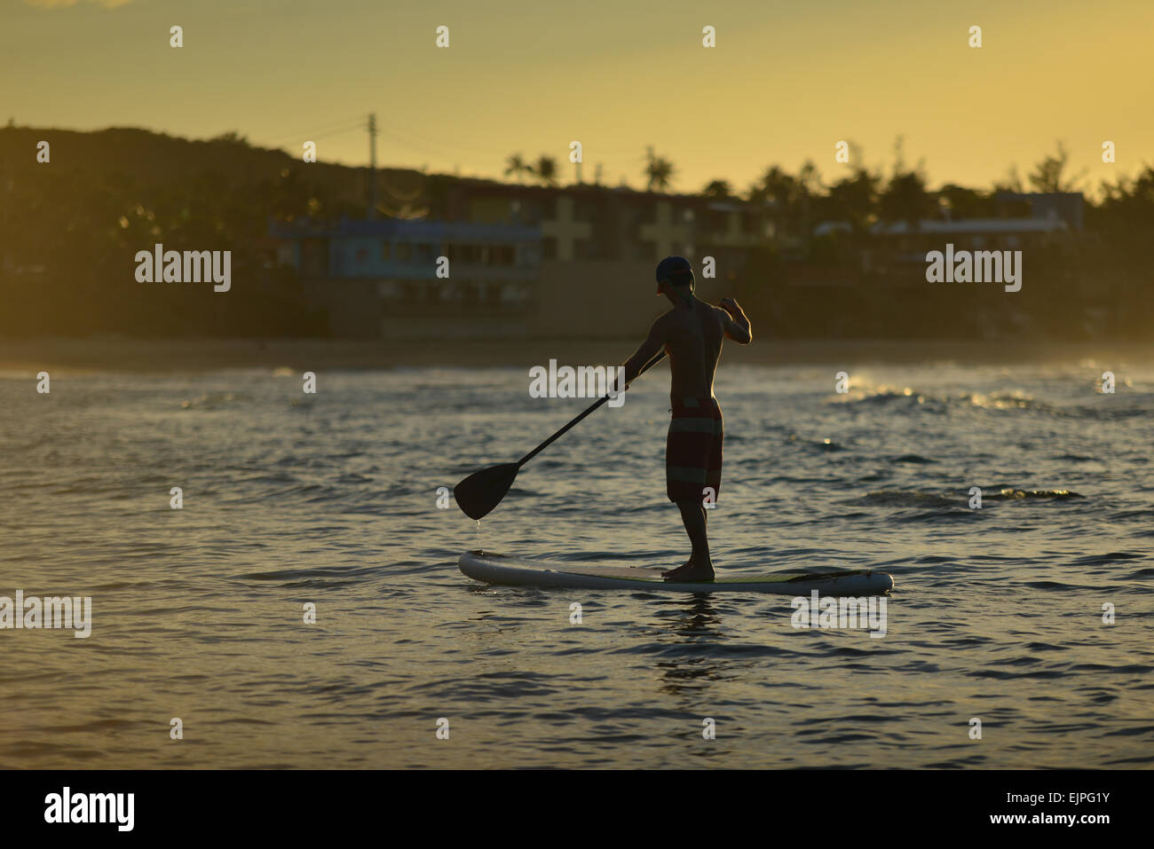 Silhouette of a man on a paddle board during a stunning sunset at Jobos ...