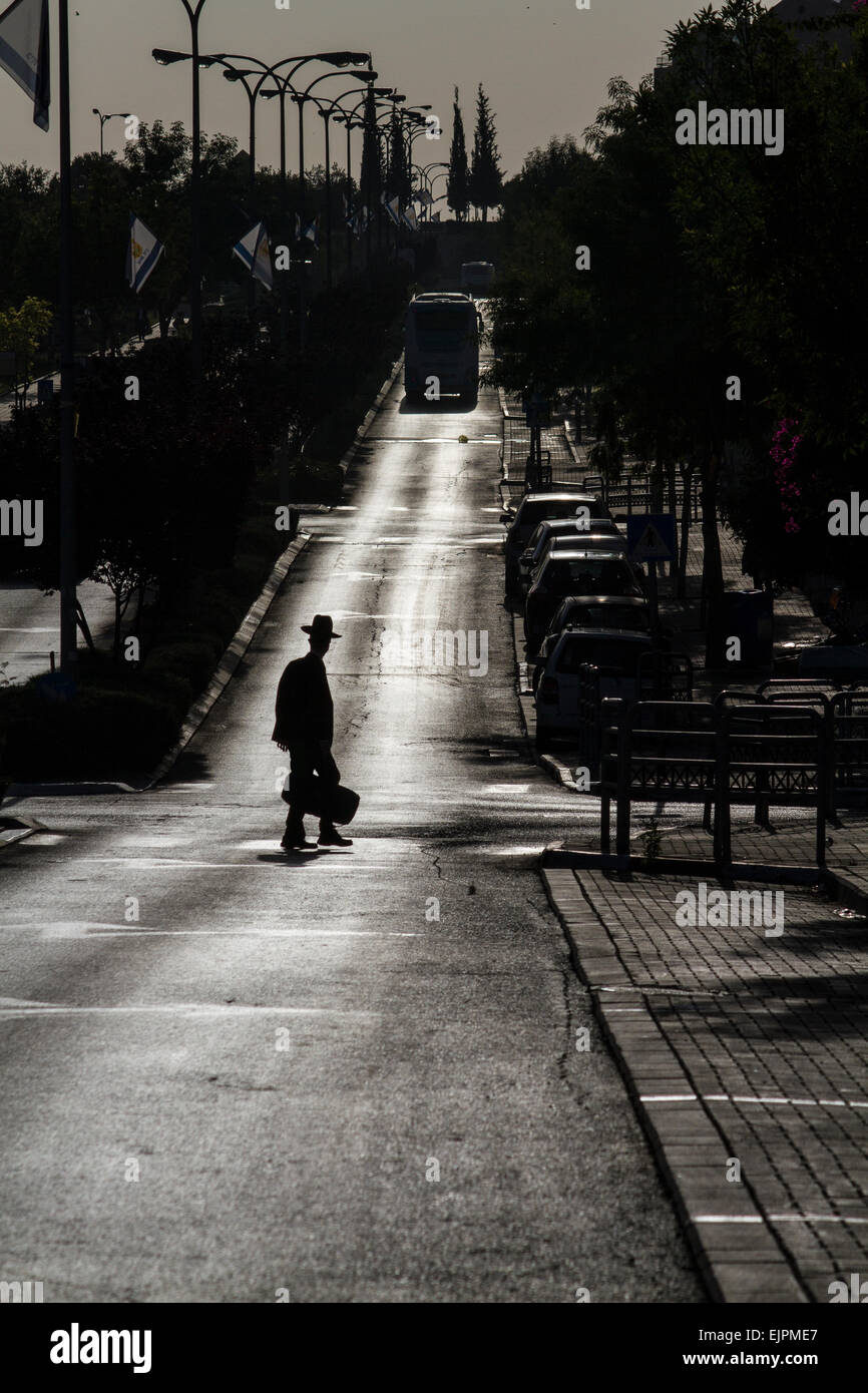 Early morning walk across road with bus and cars parked, light poles ...