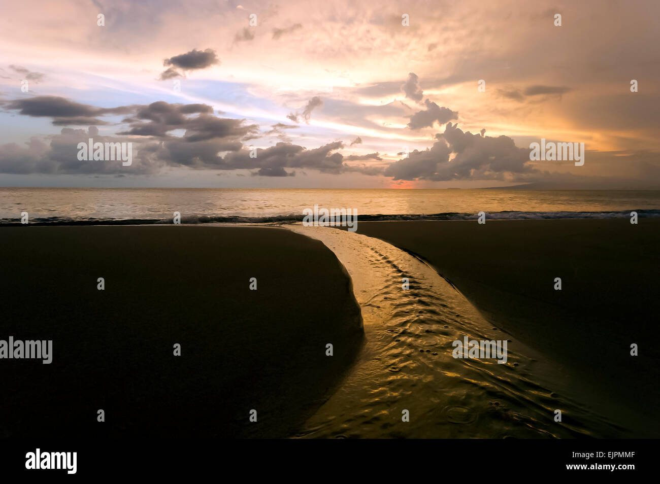A shimmering stream flows into a beautiful ocean sunset with a cloudy ...