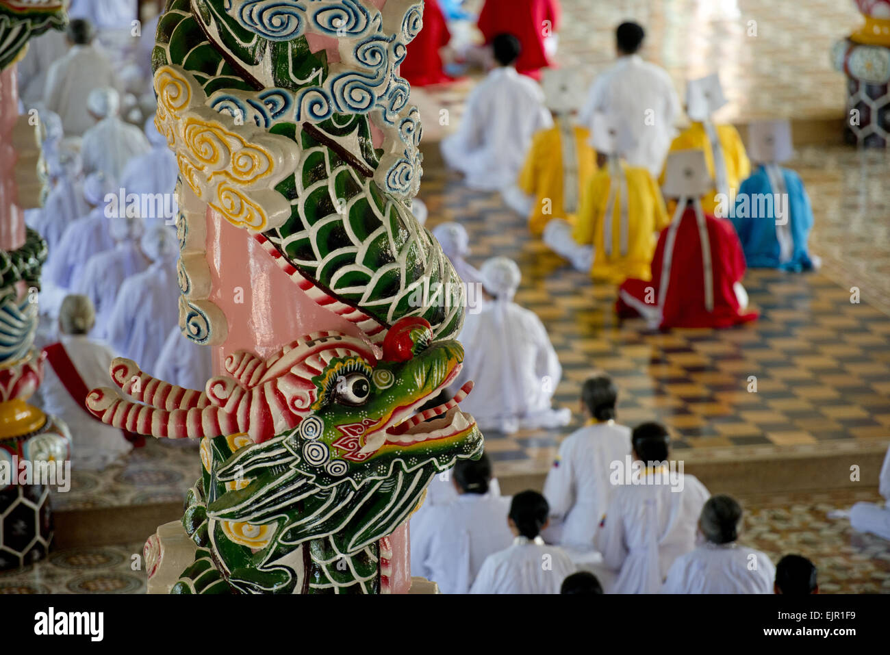 Caodaist disciples sitting beside colourful columns with dragons during ...