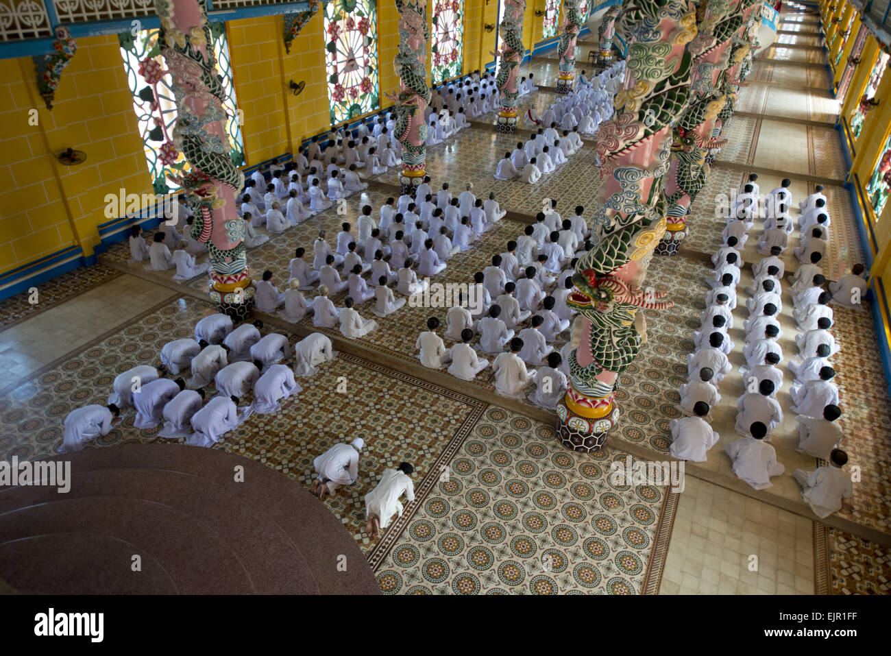 Caodaist disciples sitting beside colourful columns with dragons during ...
