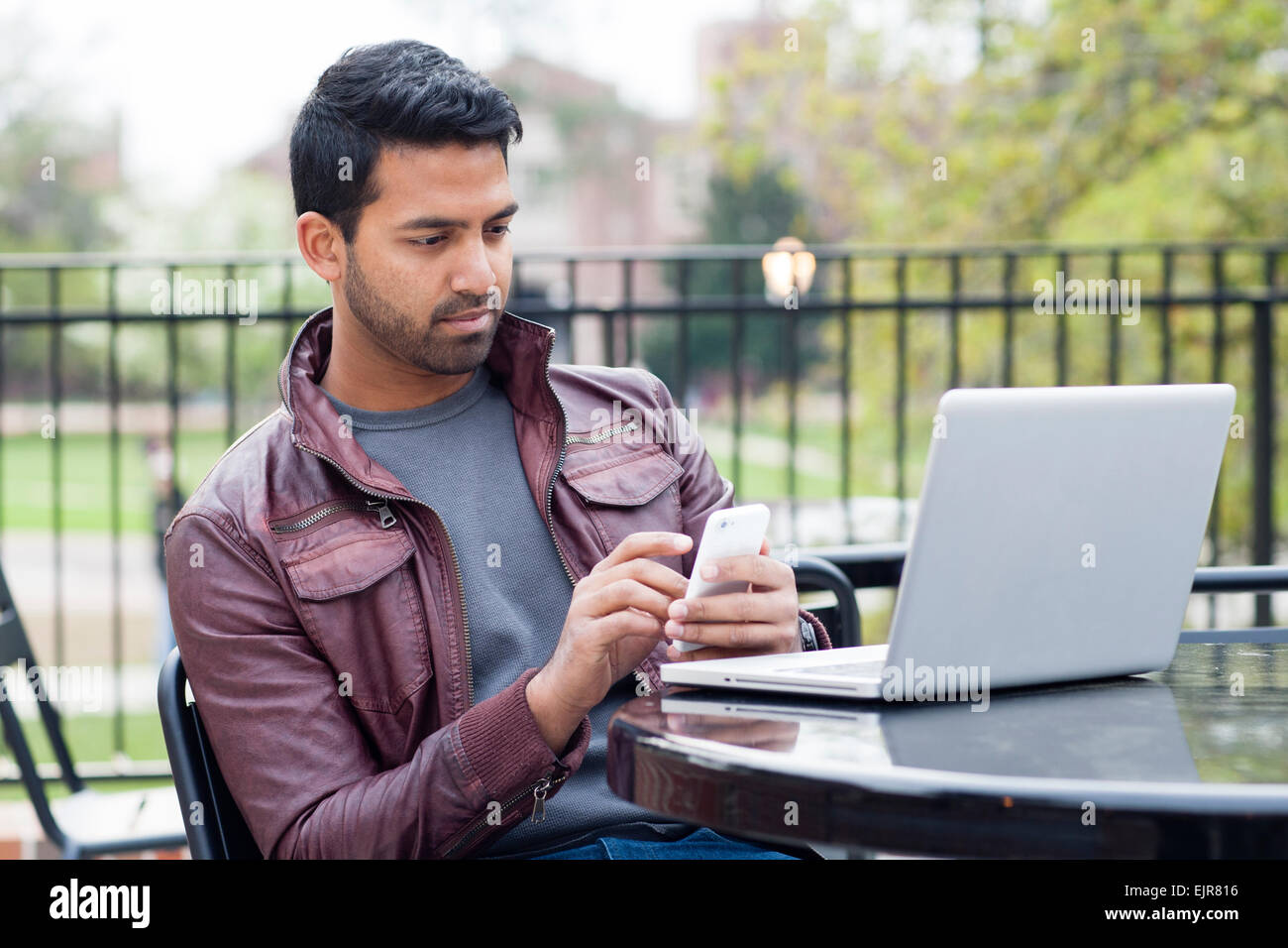 Indian man using cell phone and laptop at table outdoors Stock Photo ...