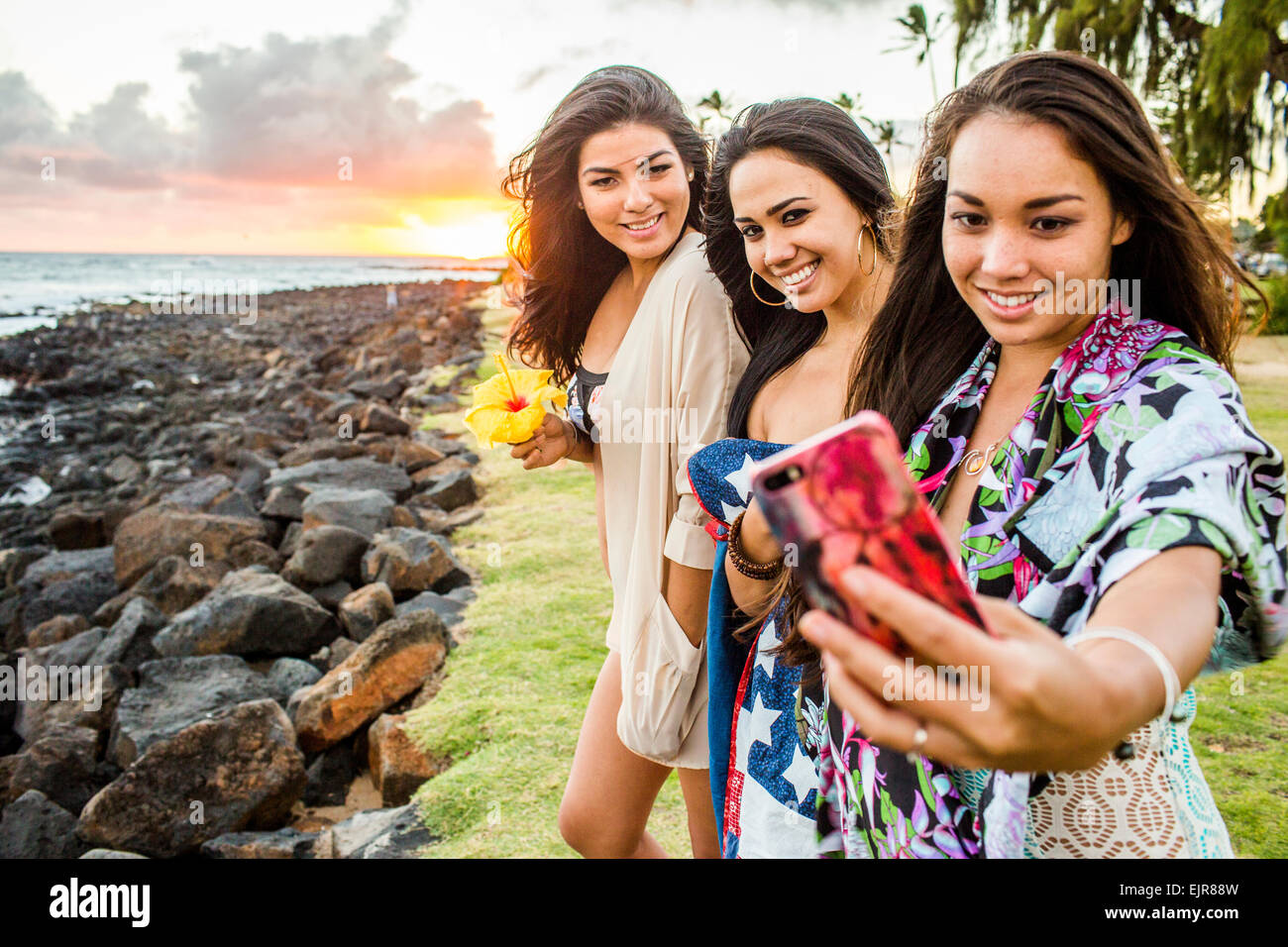 Pacific Islander women taking cell phone photograph near rocky beach ...