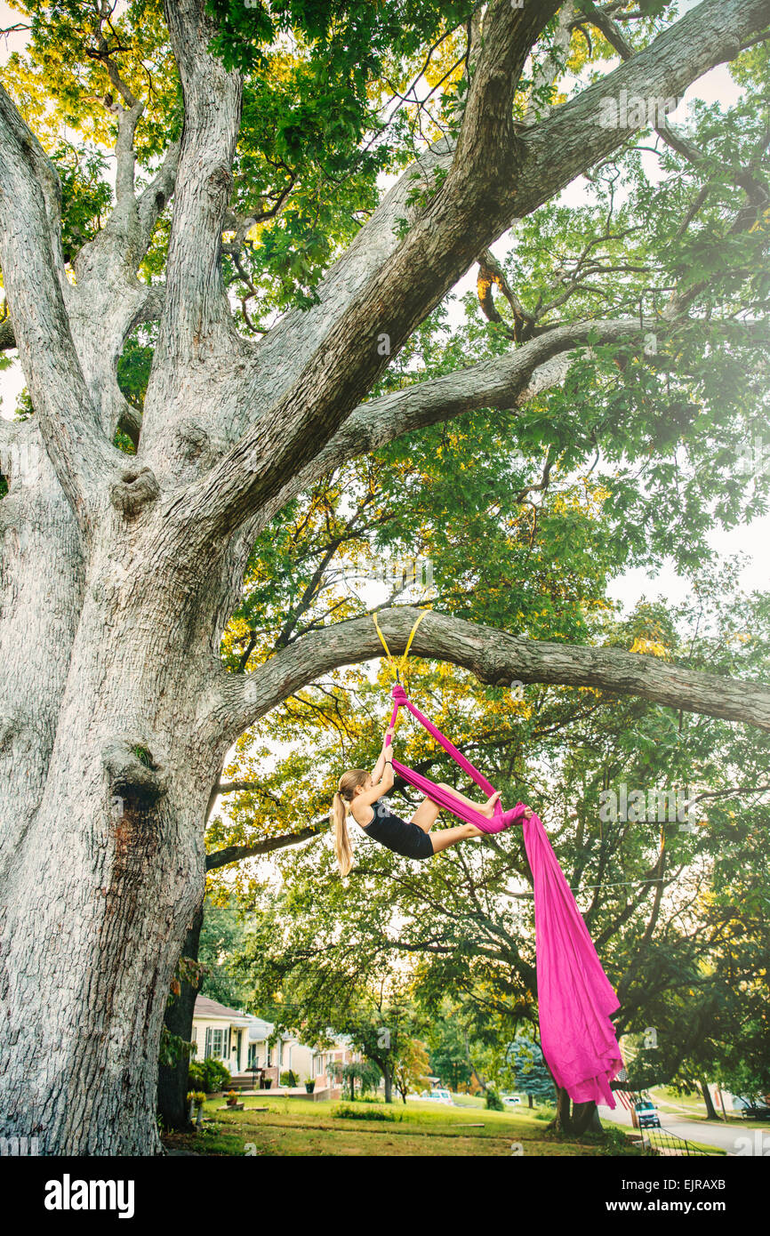 Acrobatic Caucasian girl hanging on fabric under tree Stock Photo - Alamy
