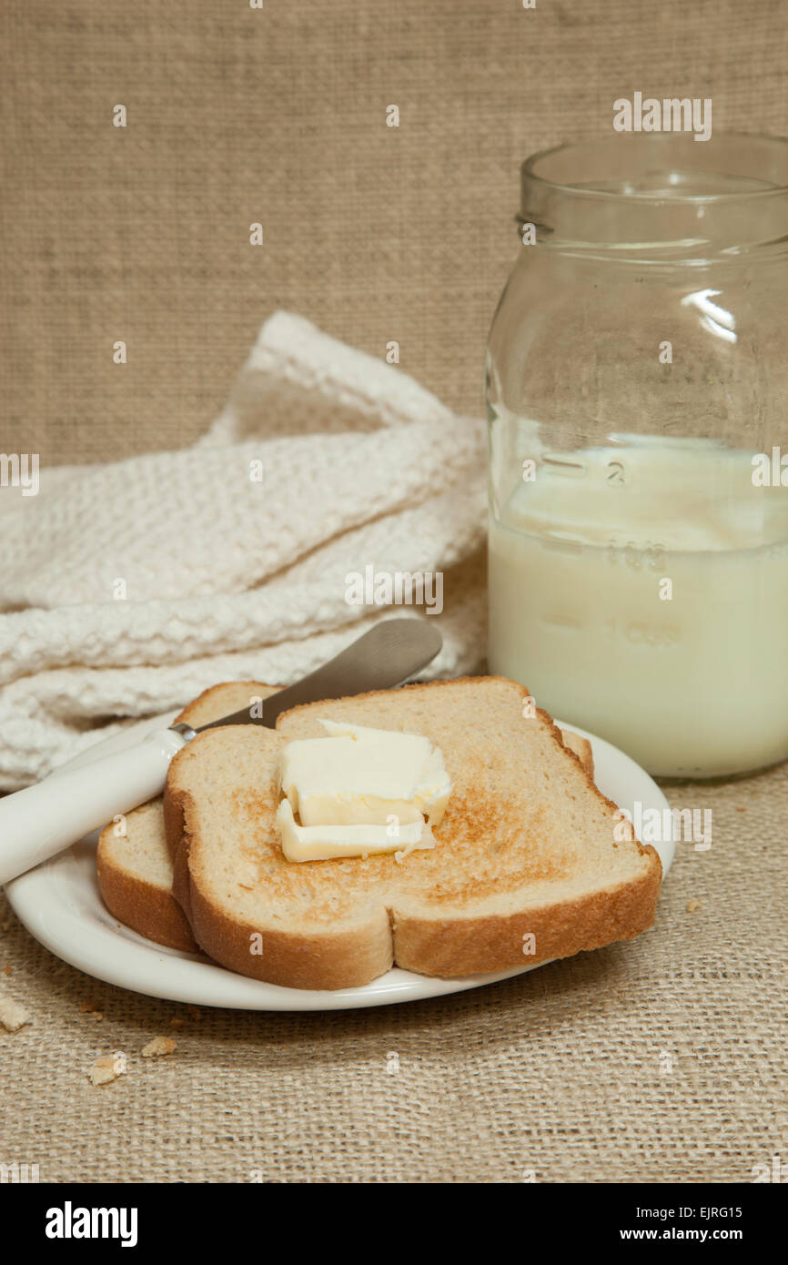 Two slices of toast rest on a cream colored plate; butter knife placed ...