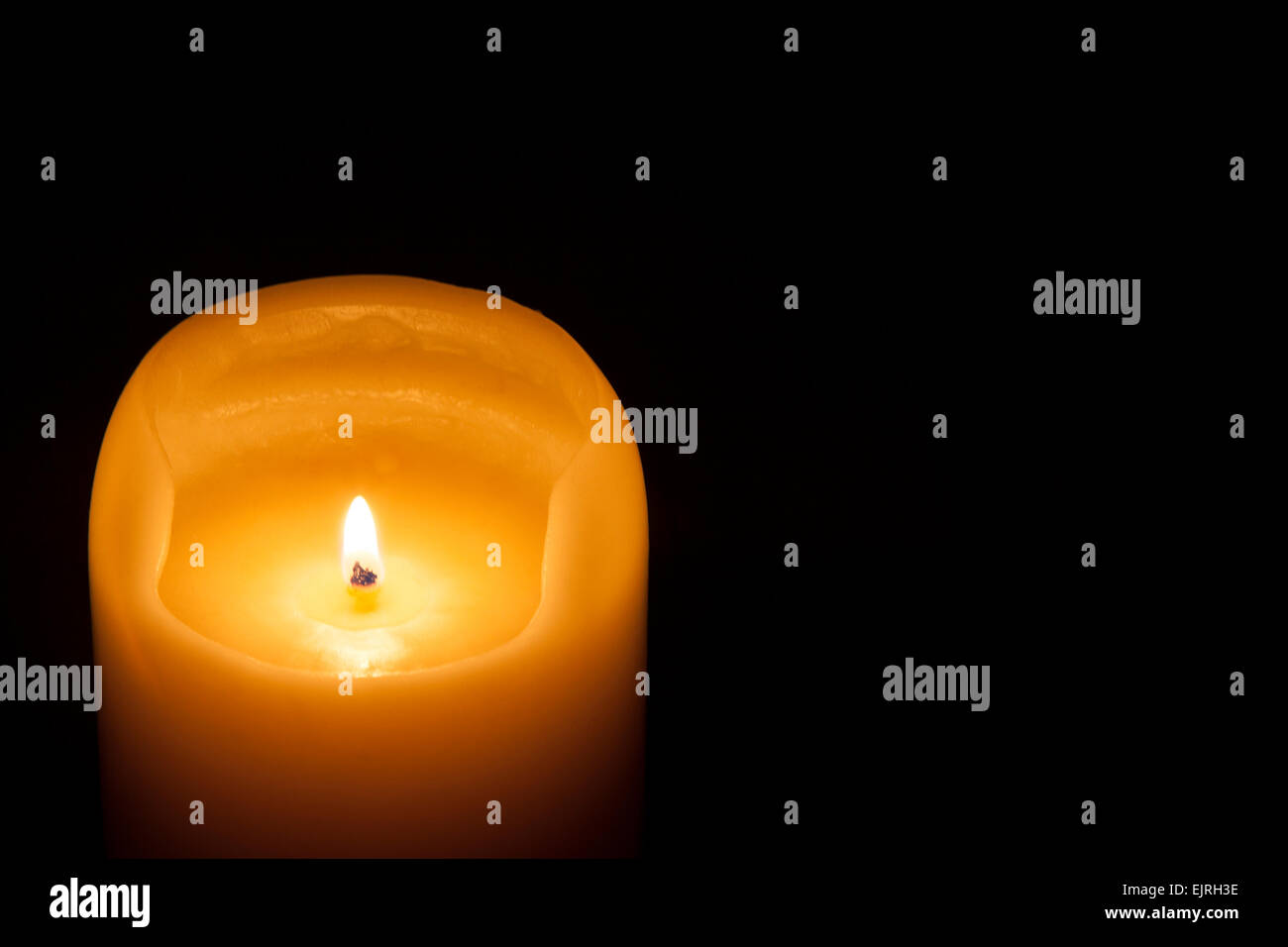 A warm glowing cream colored candle burns on a solid black background ...