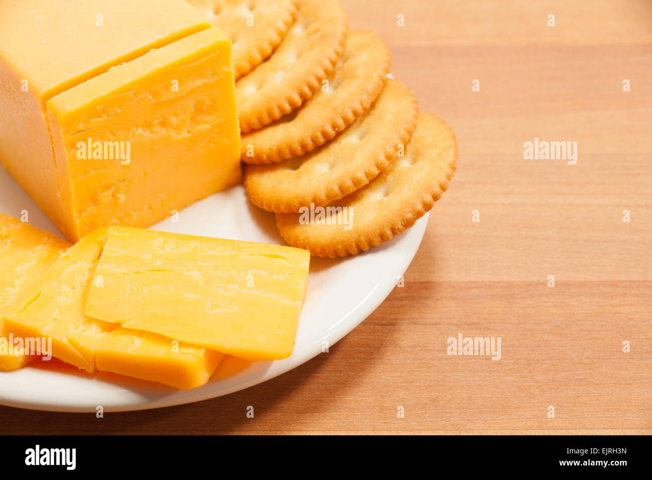 Yellow cheddar cheese is sliced on a white plate with round crackers ...