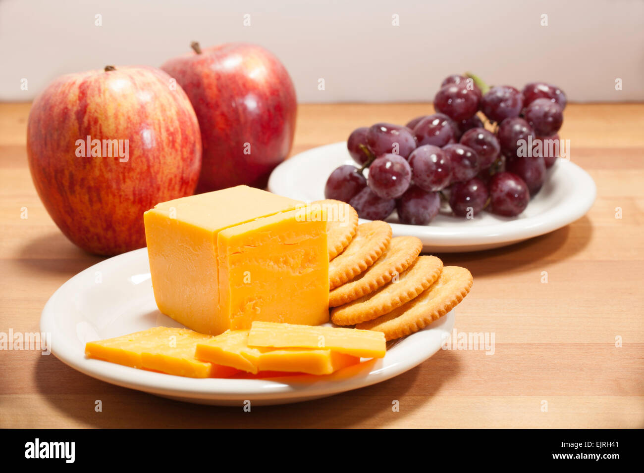 Yellow cheddar cheese is sliced on a white plate with round crackers ...