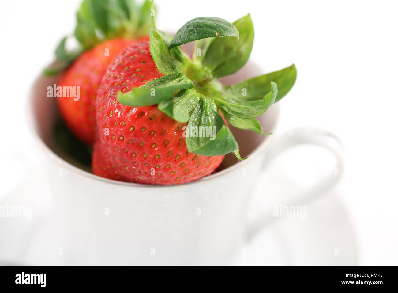 Fresh red strawberries sit inside a white china teacup atop a saucer ...