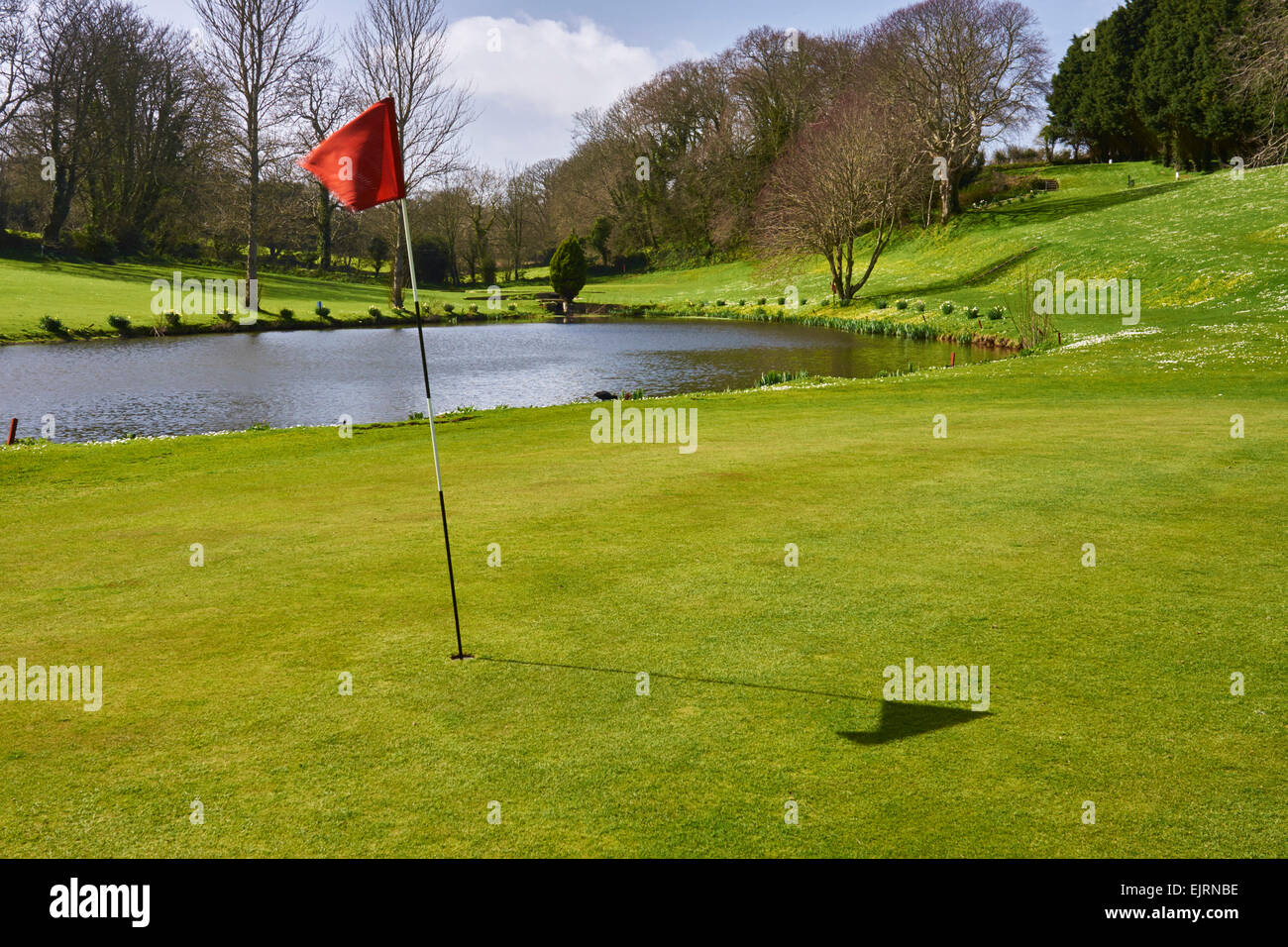 Golf Course green with red flag marker and shadow. Water hazard behind ...