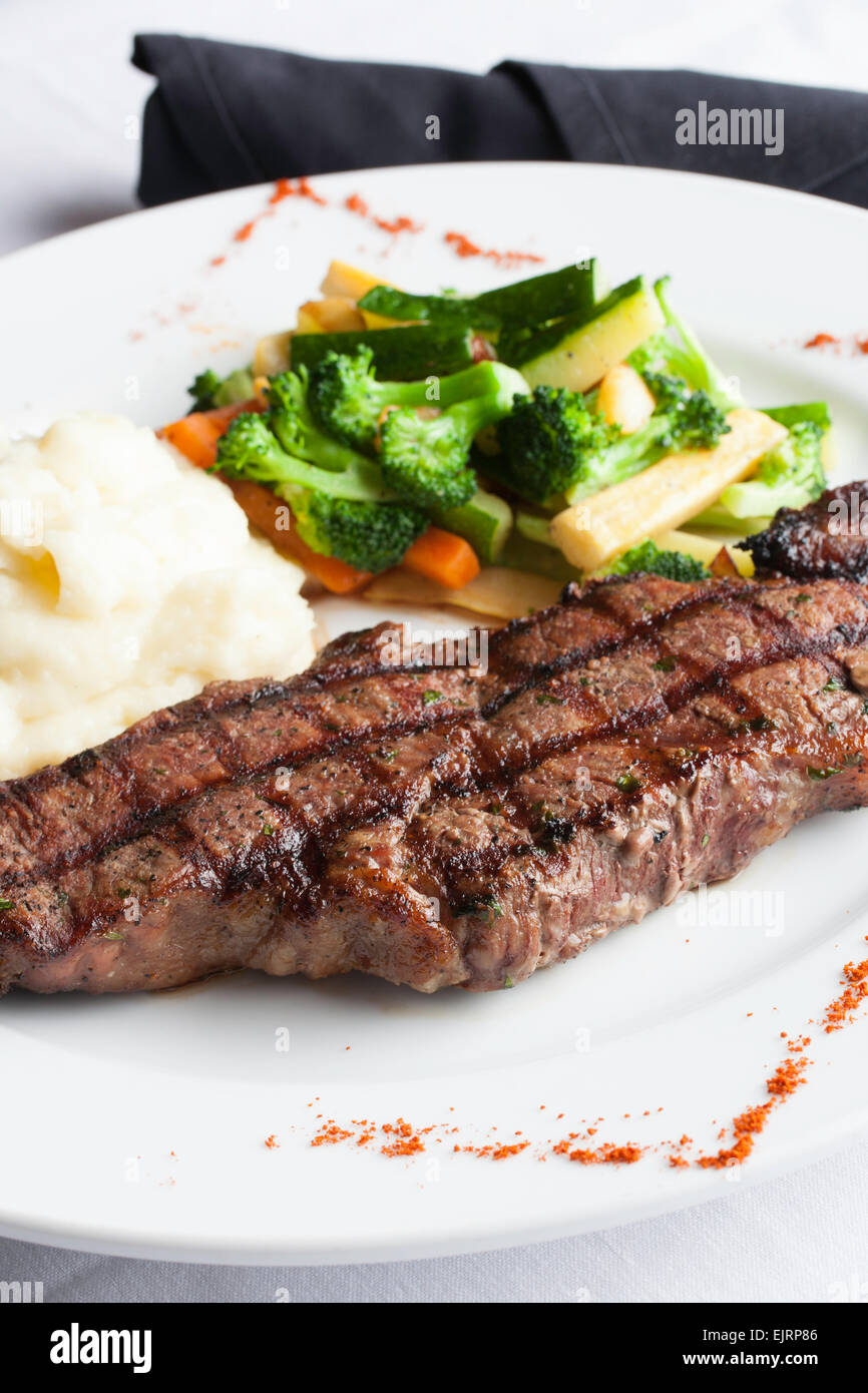 A white plate holds a delicious grilled New York Strip Steak with a ...