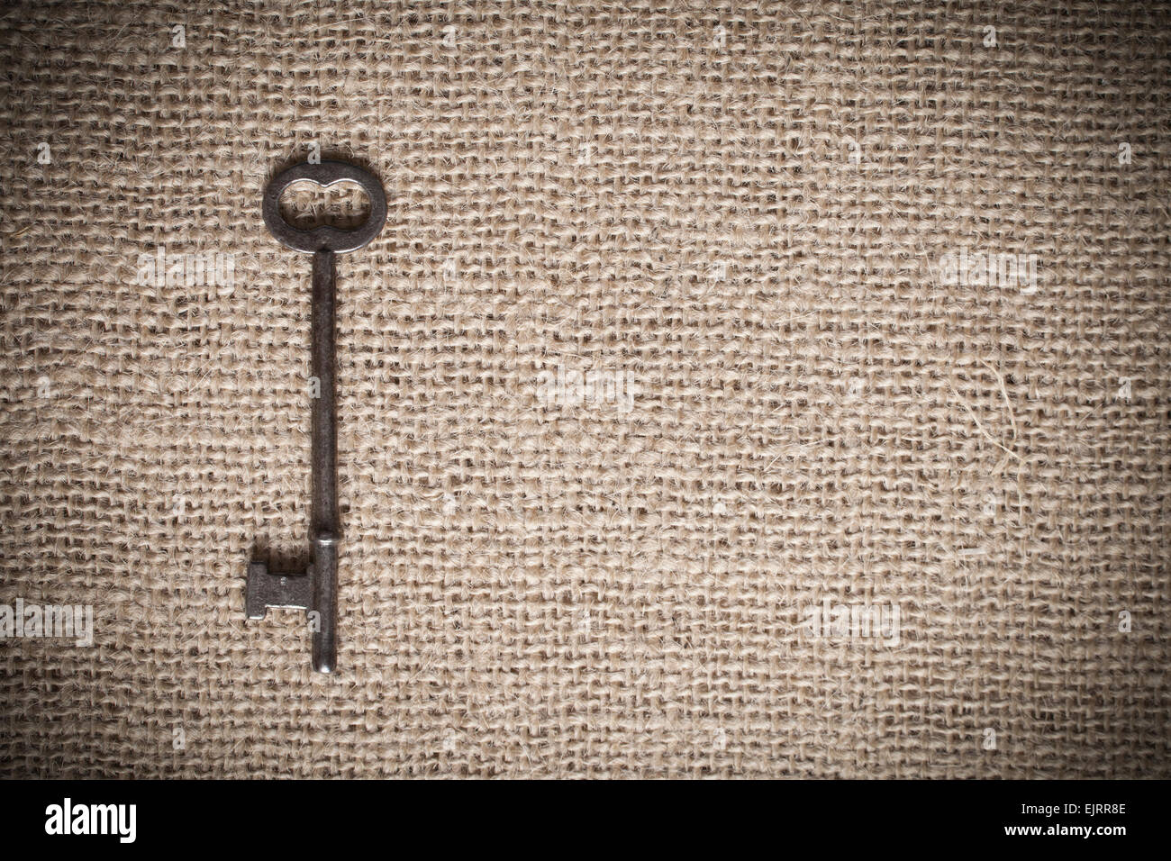 An old metal skeleton key sitting on a piece of brown burlap; horizonal ...