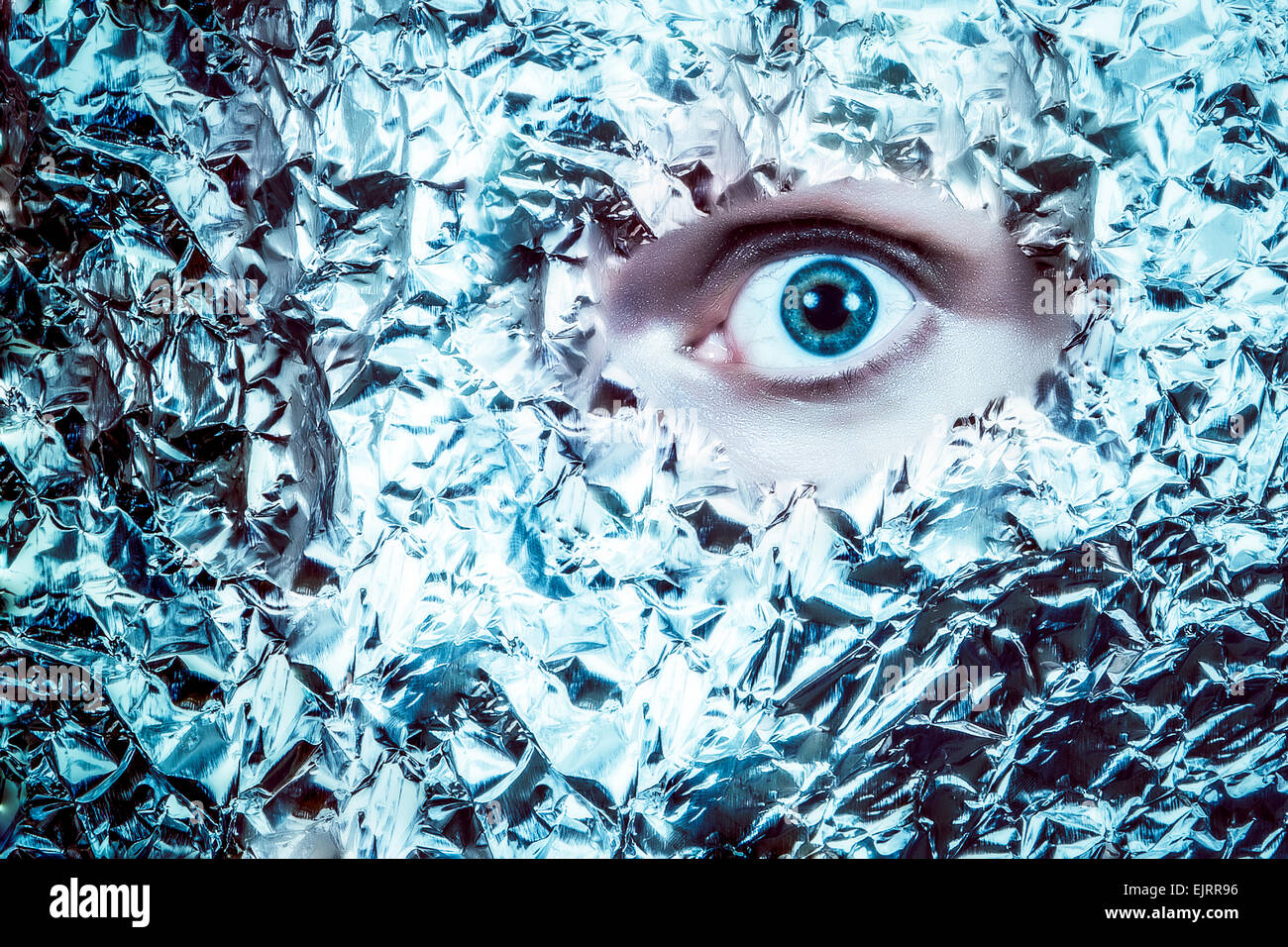 An eye peeks out of a mask of tin foil. Looks frightening and surreal ...