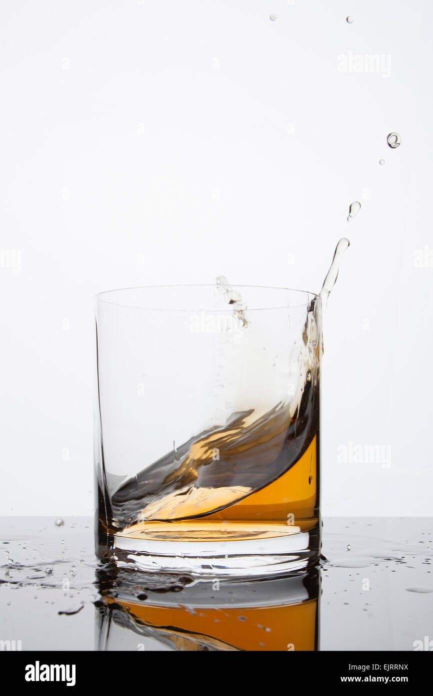 A rocks glass with Whisky sits atop a reflective surface on a bright ...