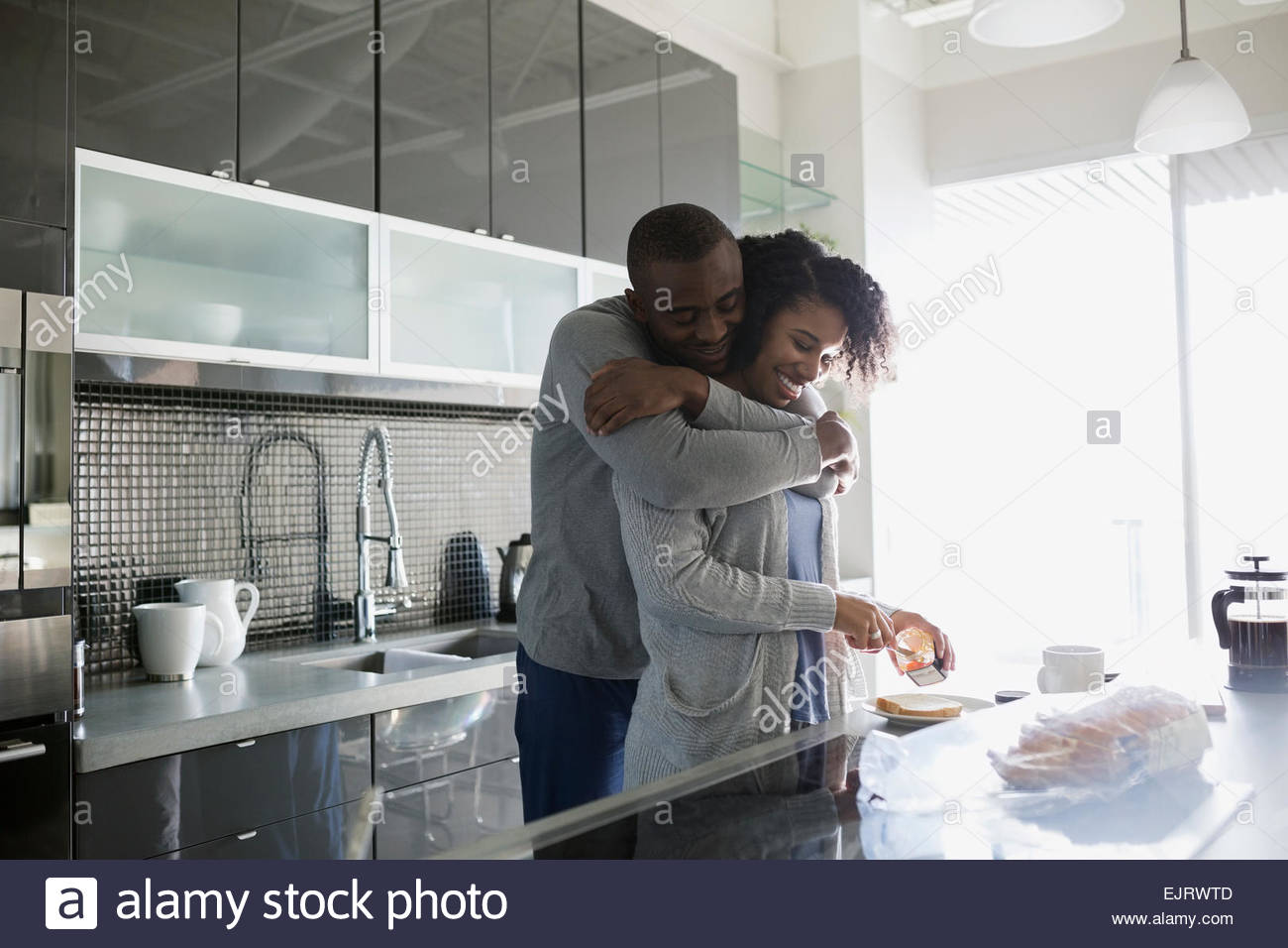 Smiling couple hugging and making breakfast in kitchen Stock Photo - Alamy