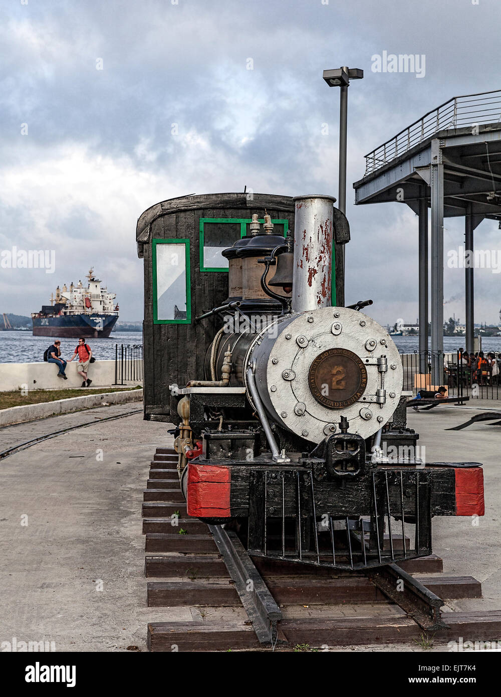 Steam train in the harbour in Havana with two people sitting on a wall ...