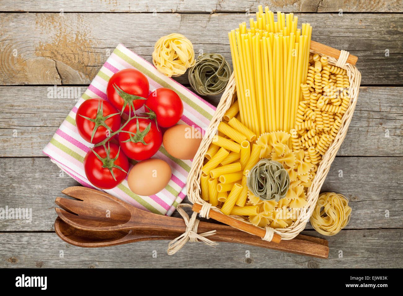 Various pasta, tomatoes and kitchen utensils on wooden table background ...