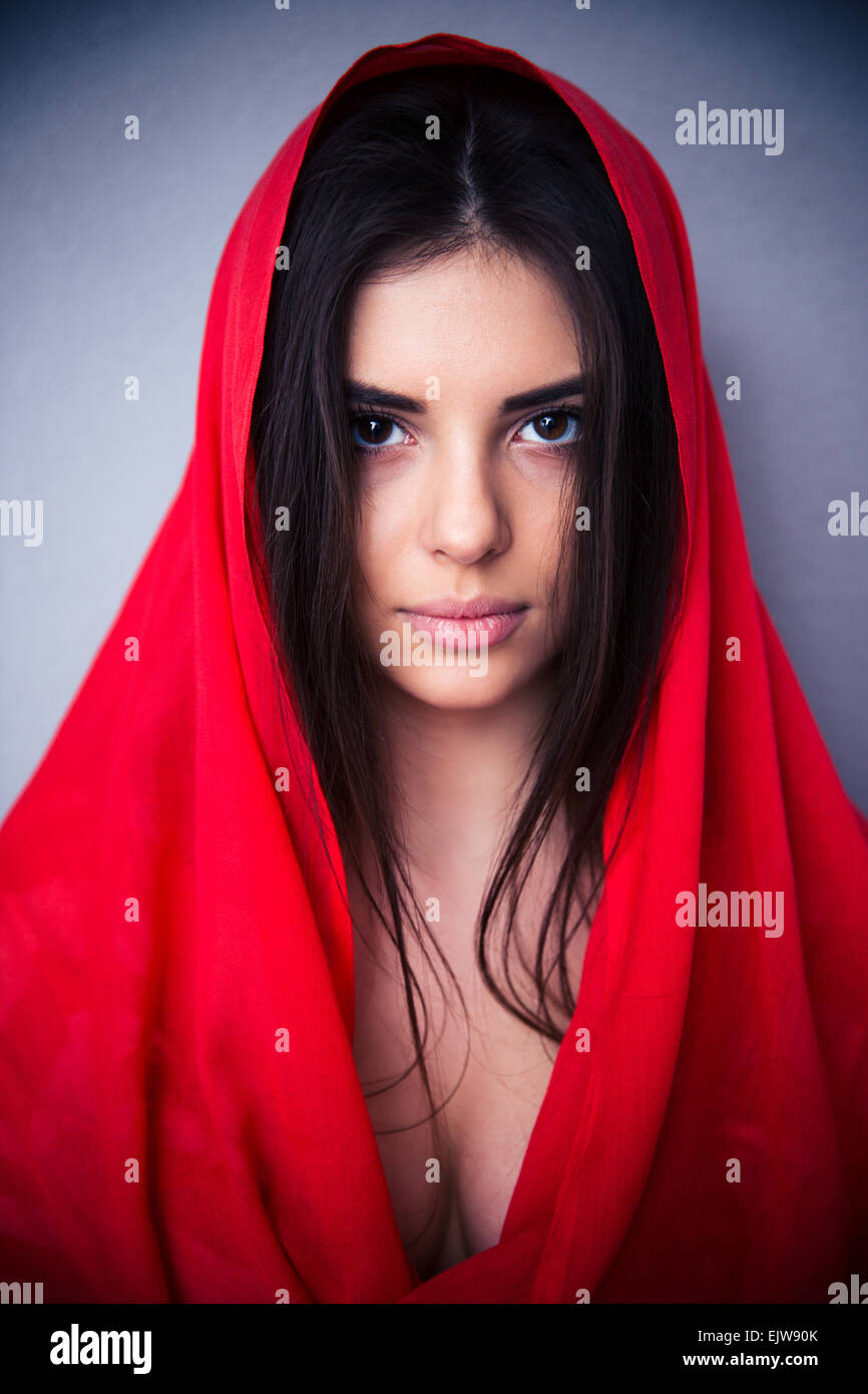 Portrait of cute young woman in red cloth over gray background. Looking ...