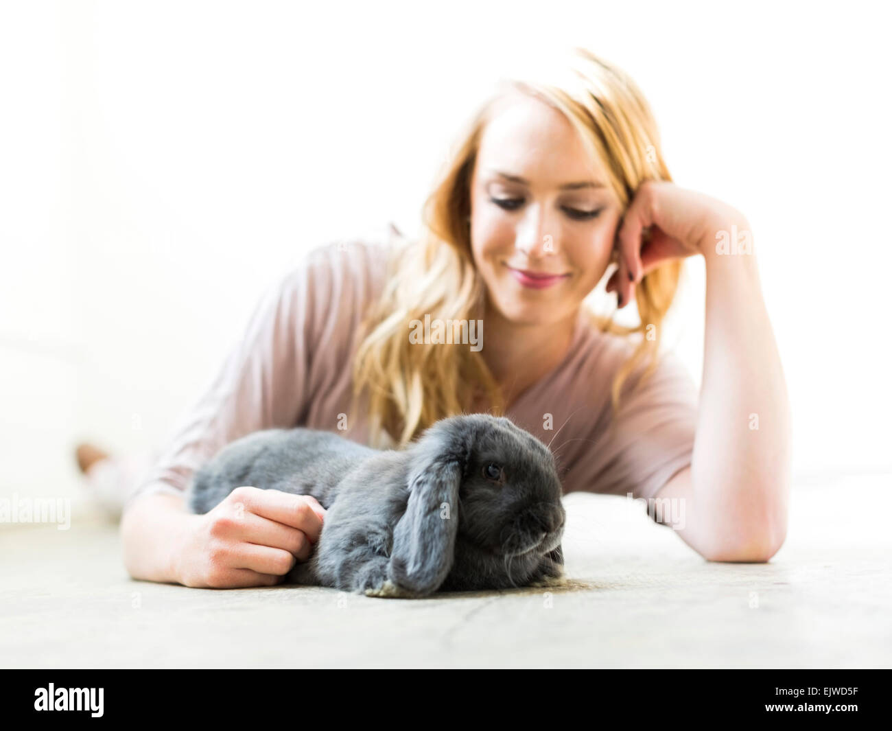 Young woman lying on floor and stroking rabbit Stock Photo - Alamy
