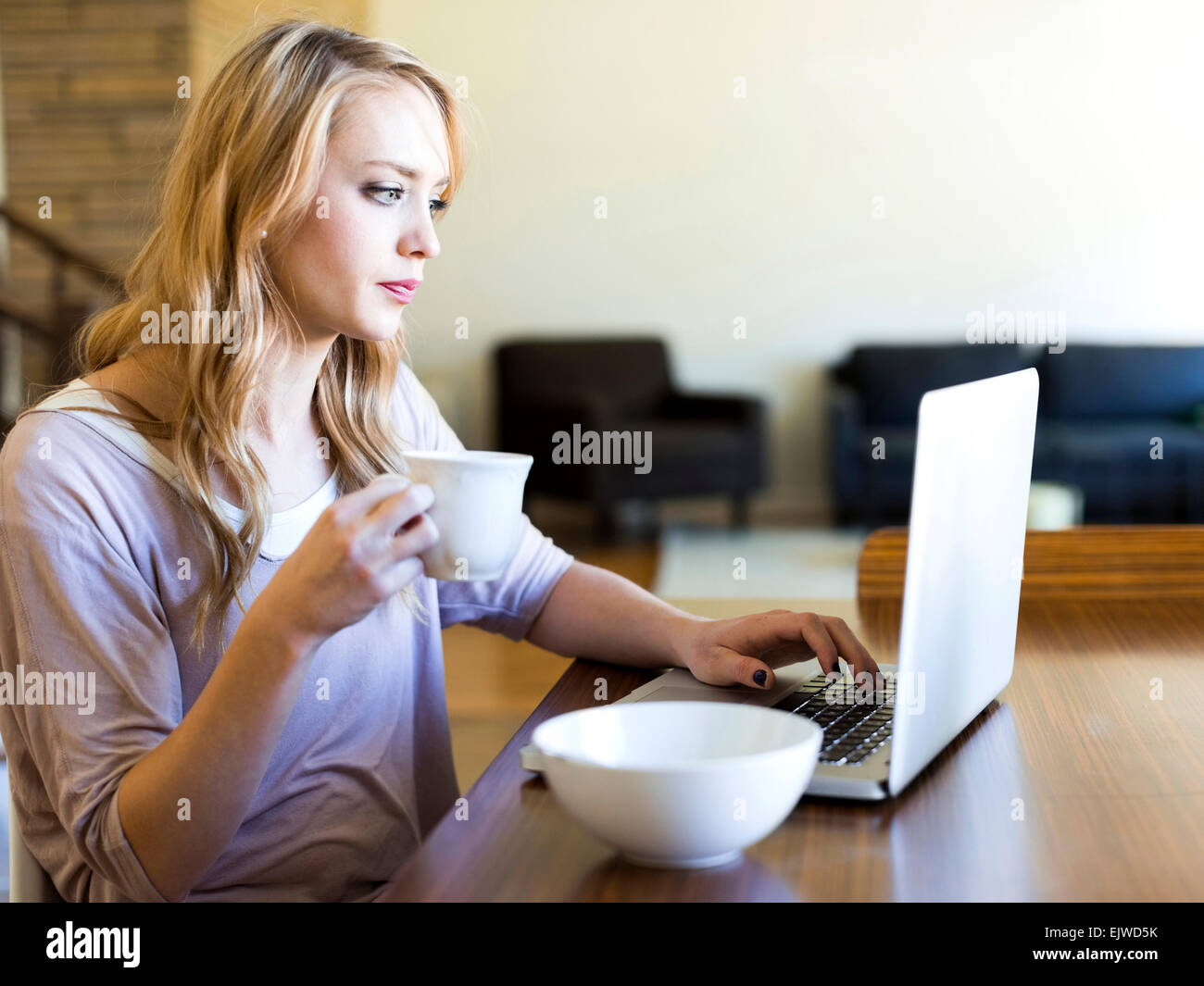 Young woman using laptop and drinking coffee at table Stock Photo - Alamy
