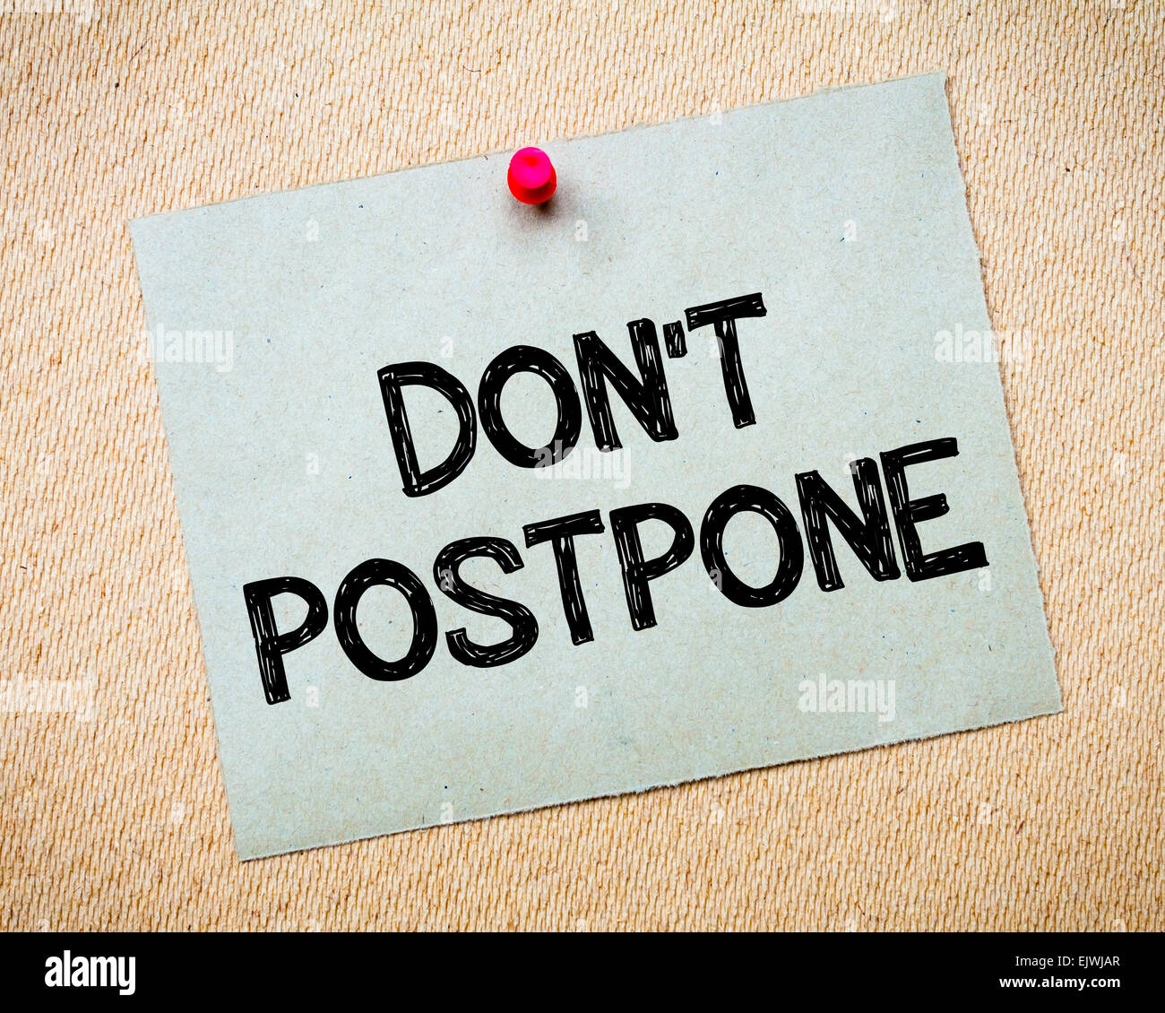 Recycled paper note pinned on cork board.Don' t Postpone Message ...