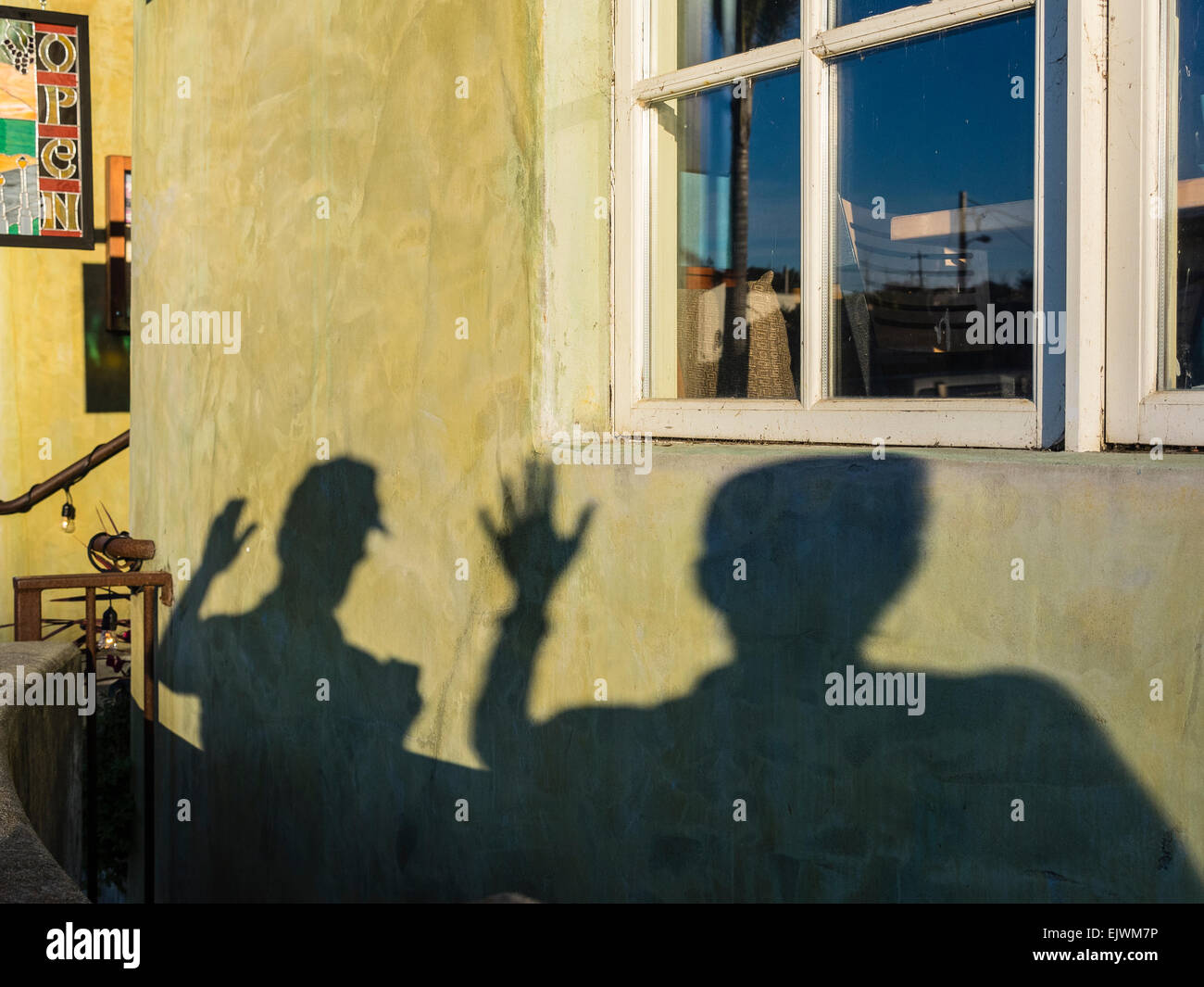 2 people hold up their hands as their shadows are cast on a light green ...