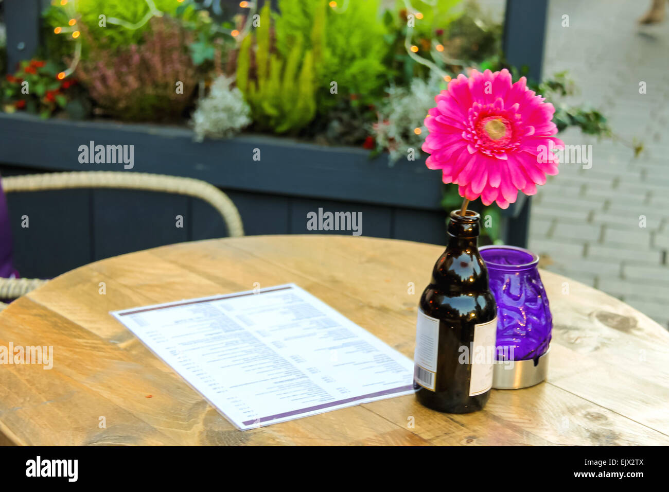 Flower in a bottle, candle and menus on the table in an outdoor cafe ...