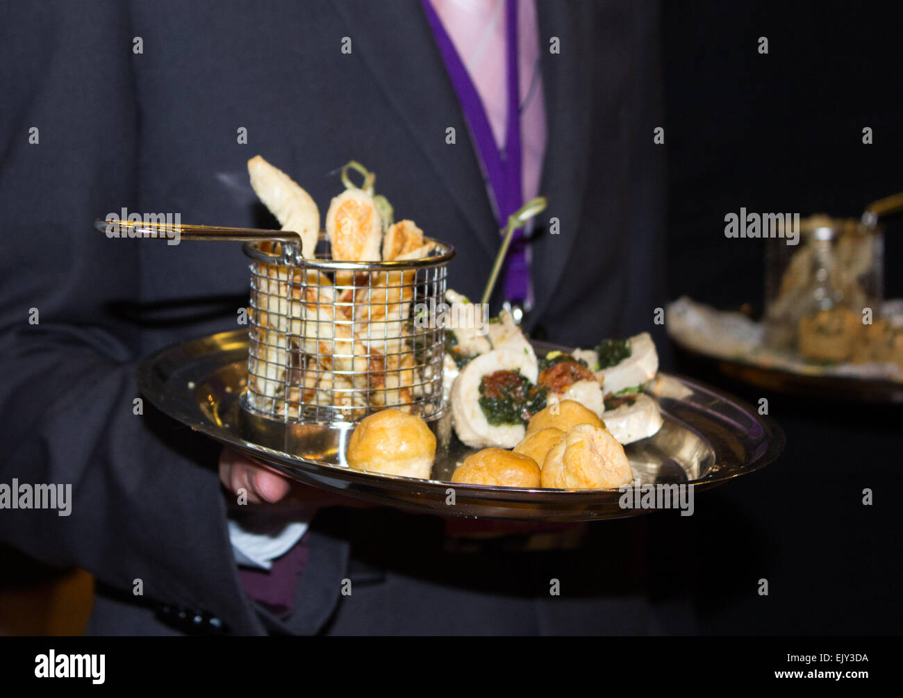 Male trainee caterer serving canapés consisting of stuffed chicken ...
