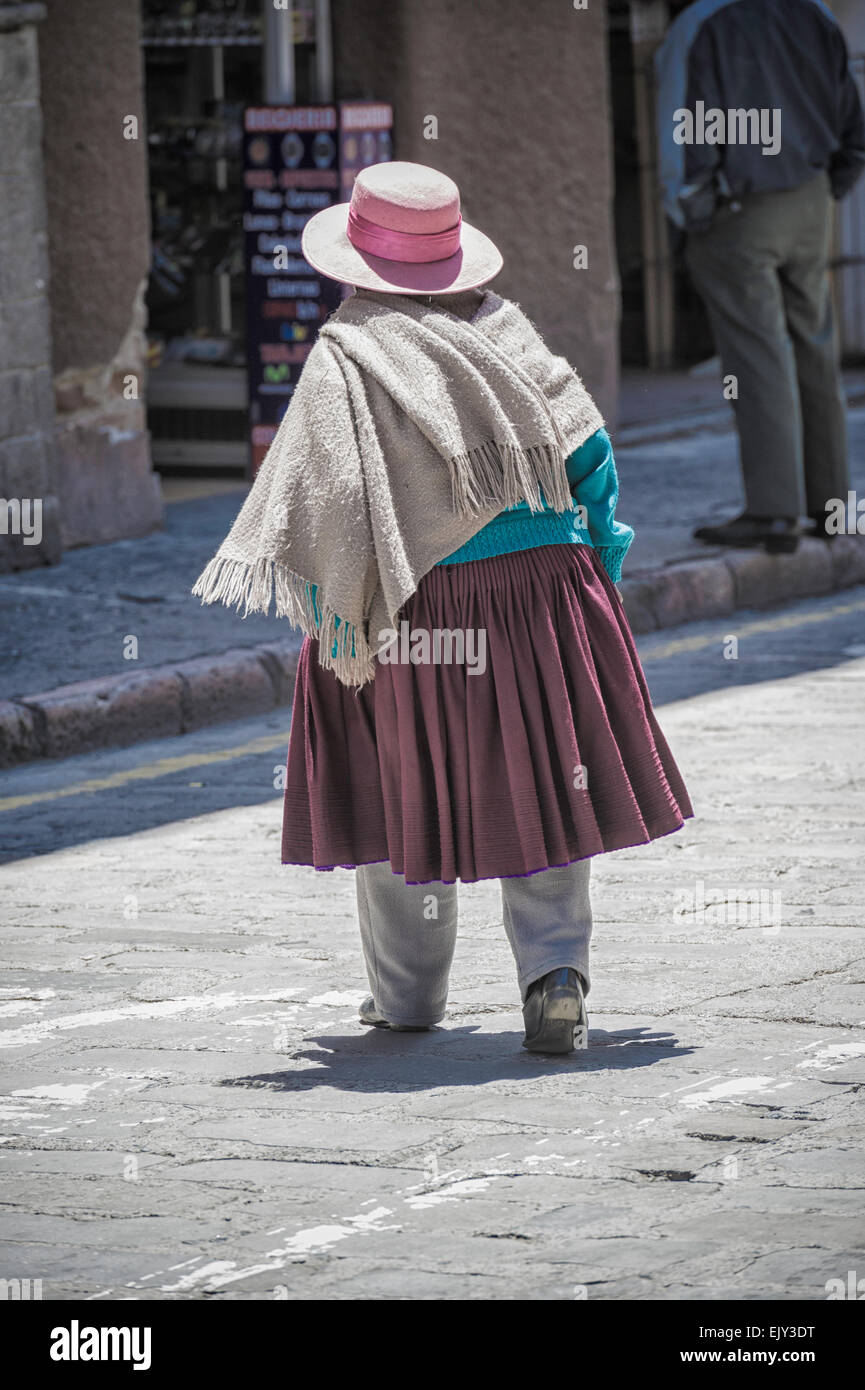 A person wearing traditional Andean clothing walks down a cobblestone ...