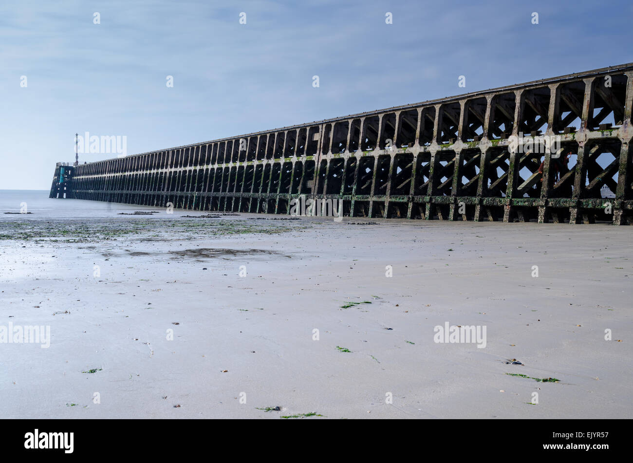 Concrete and wood breakwater stretches across sand and sea at low tide ...