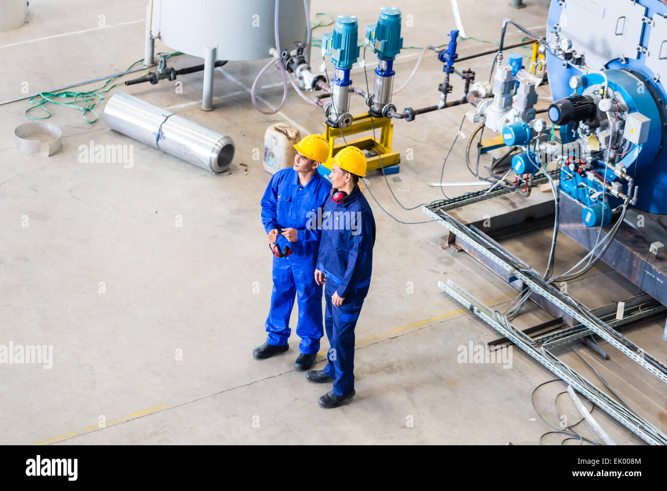Two workers in industrial factory discussing in front of machines, top ...