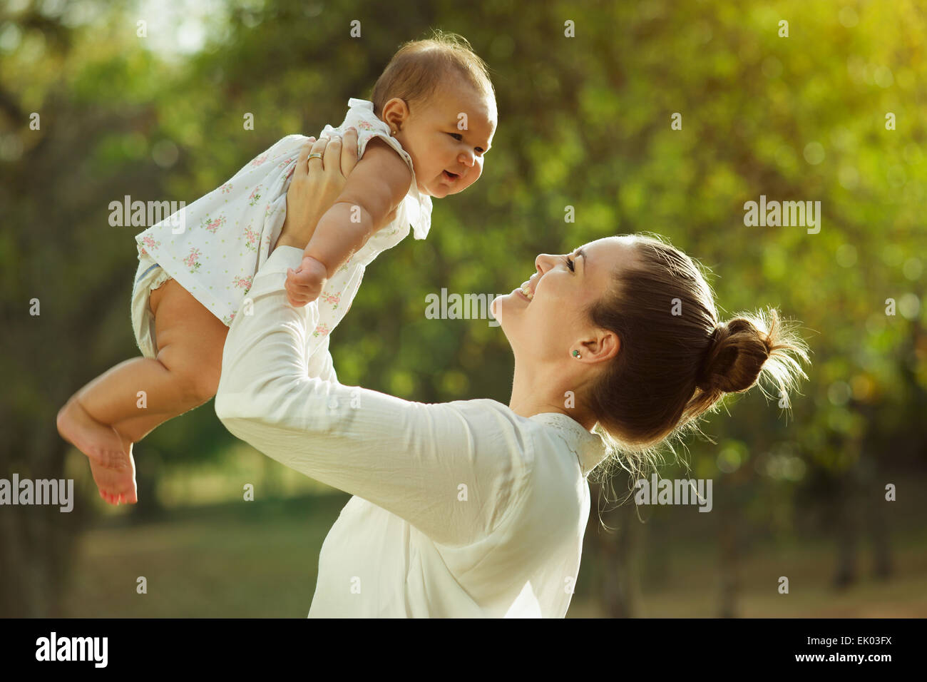 Beautiful woman lifts high her adorable baby up mid air and looks at ...