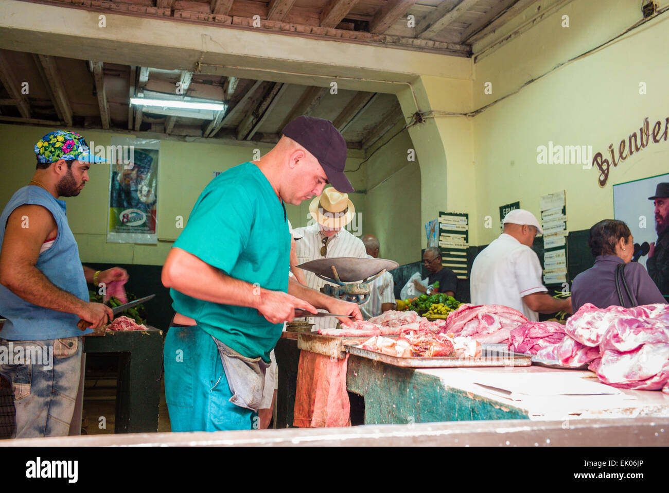 Butcher cuts meat in a government sponsored market with a poster of ...