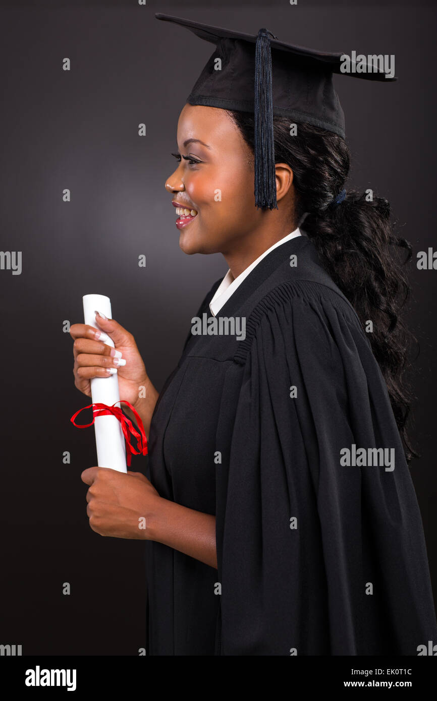 side view of happy young African female graduate on black background ...