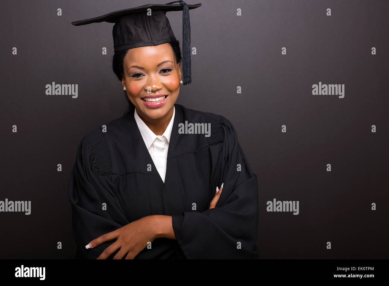 beautiful female college graduate with arms crossed on black background ...