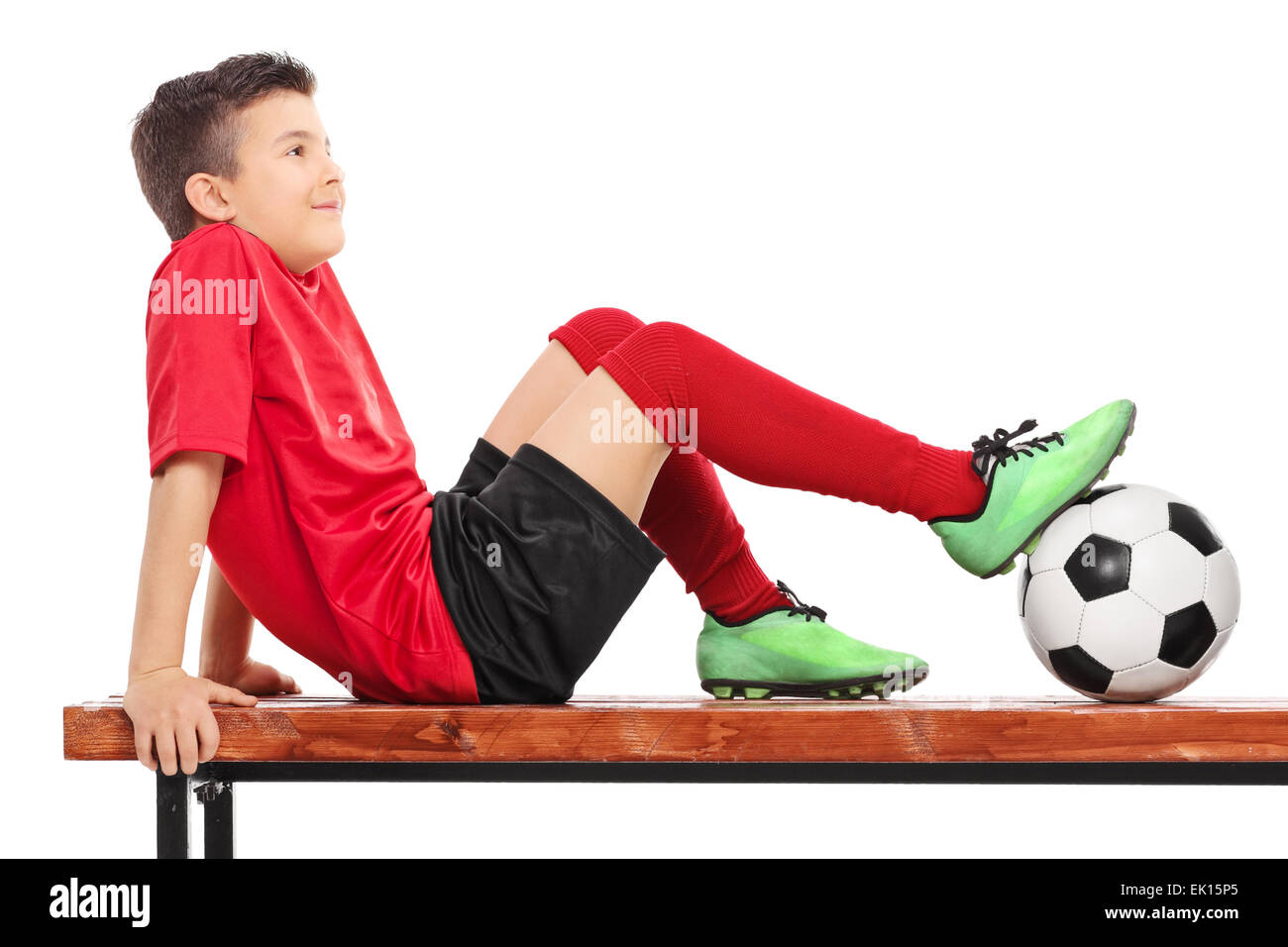 Relaxed young boy in football uniform sitting on a wooden bench and ...