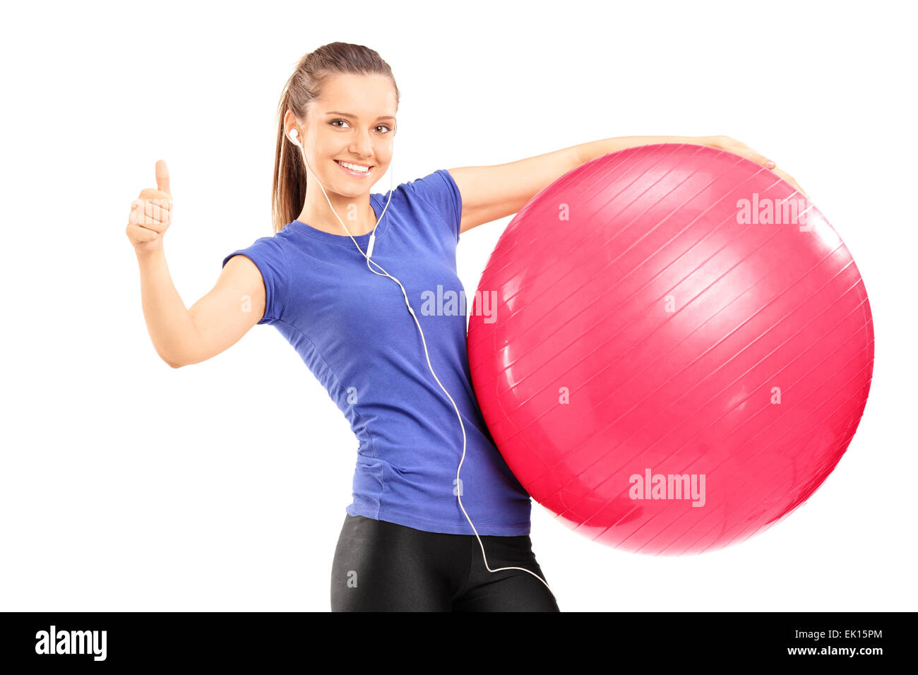 Smiling young woman holding a red exercise ball and giving a thumb up ...