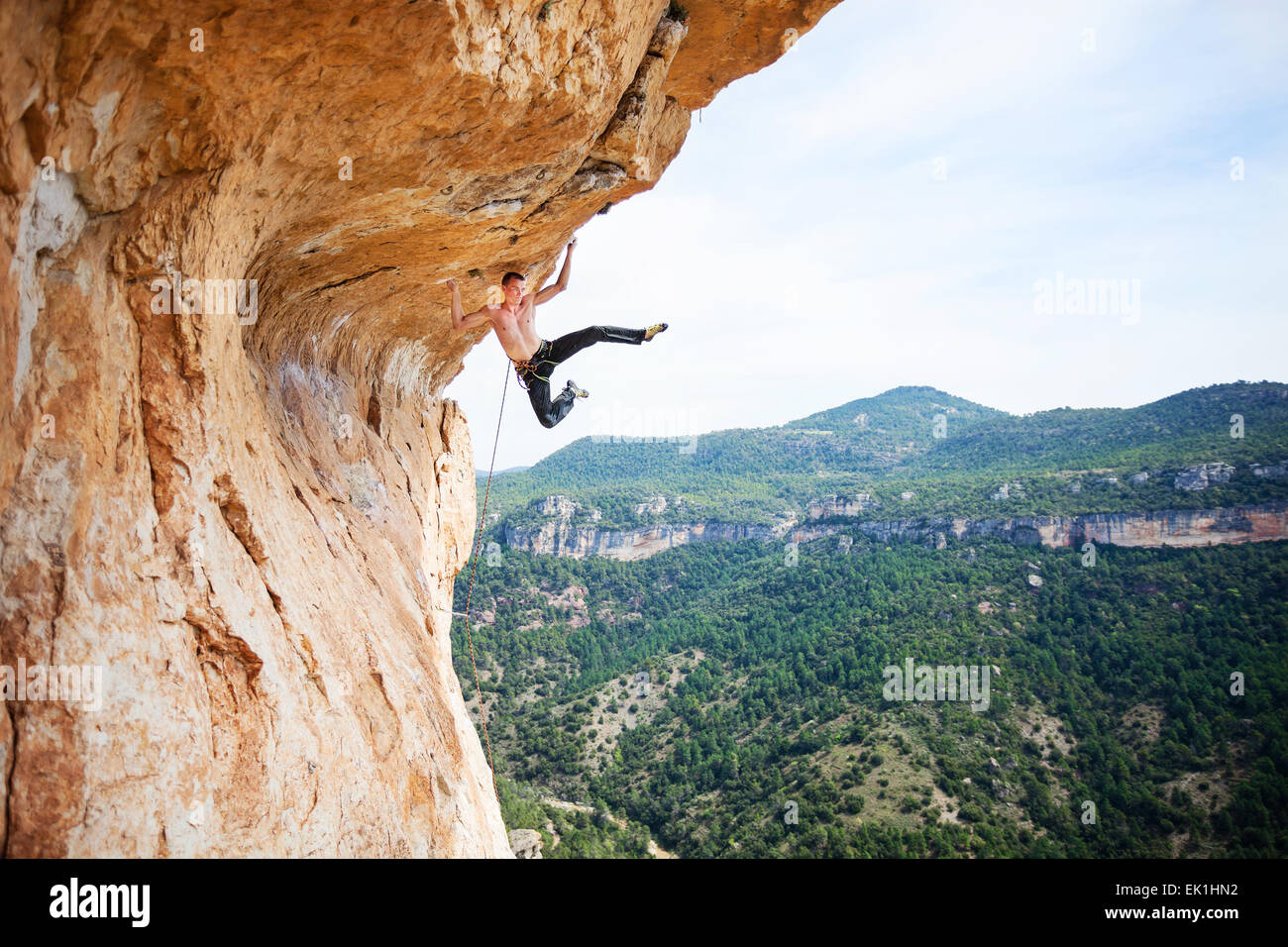 Young man climbing up ledge of cliff, on challenging part of route ...