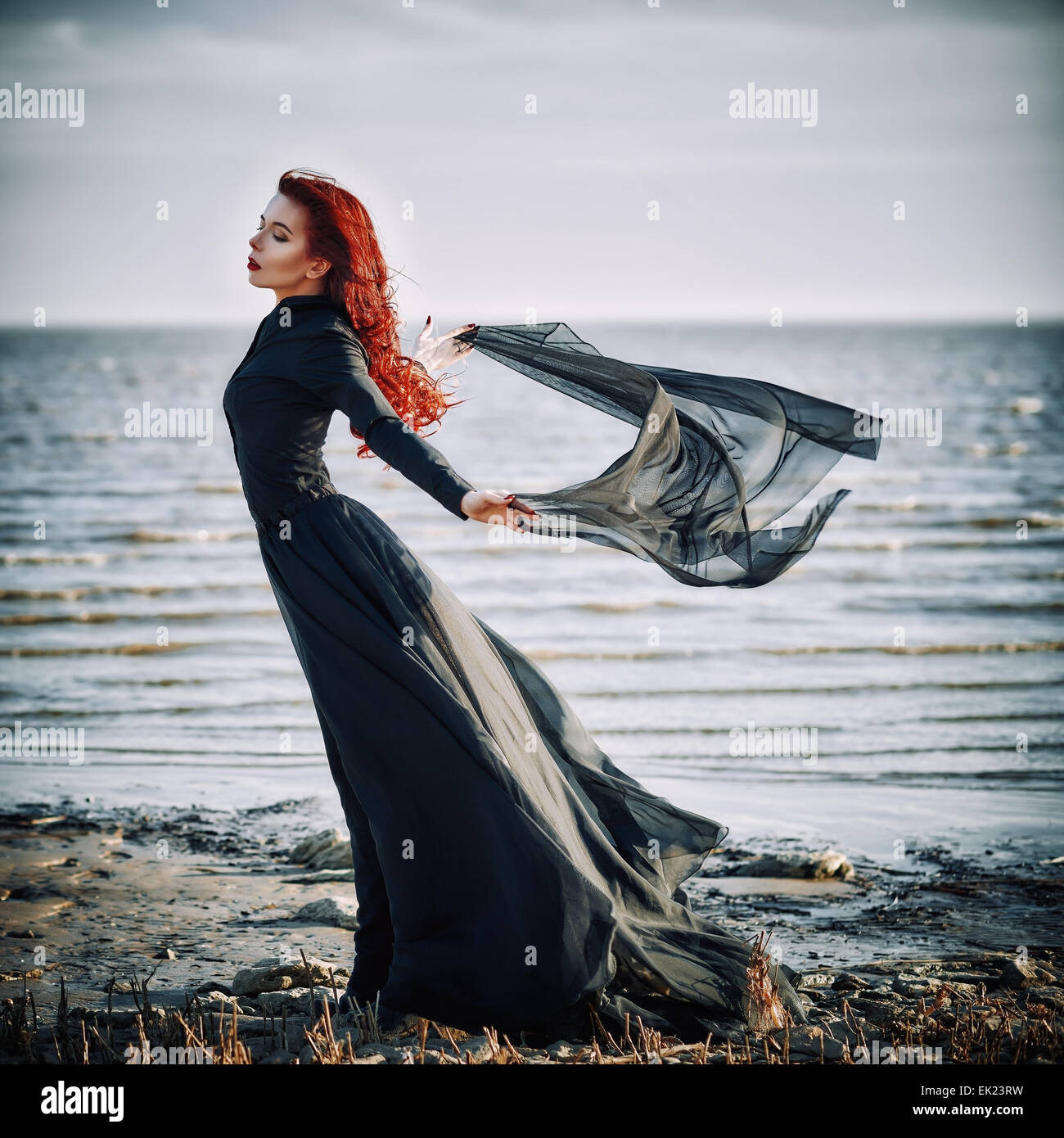 Beautiful sad goth girl with cloth in hands standing on the sea shore ...