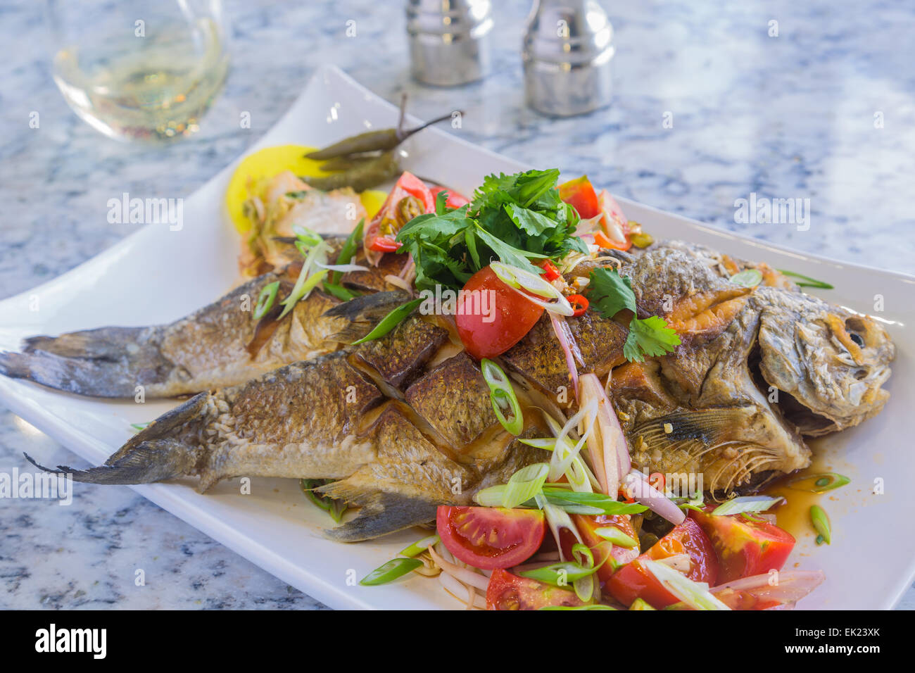 Fried whole fish served with tomato salad Stock Photo - Alamy