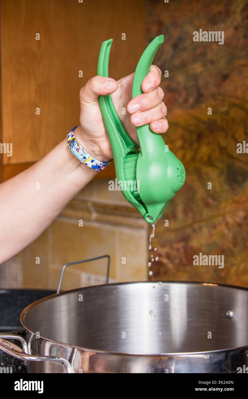 Woman using a lemon squeezer to add lemon juice to a pot of apricot jam ...