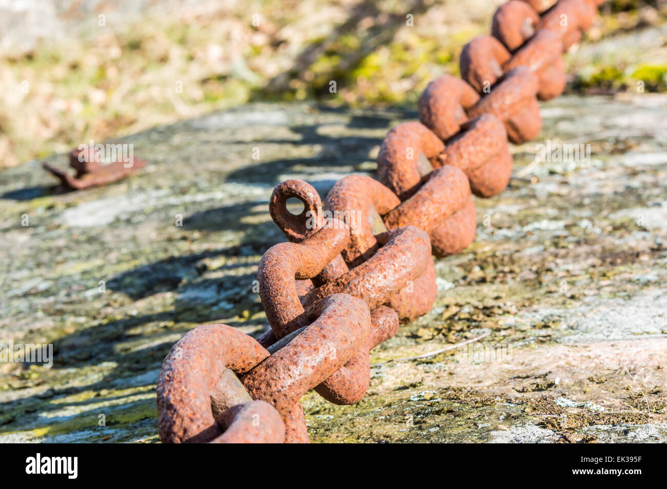 Old, big rusty iron chain on granite hill side. Sunlight creates fine ...