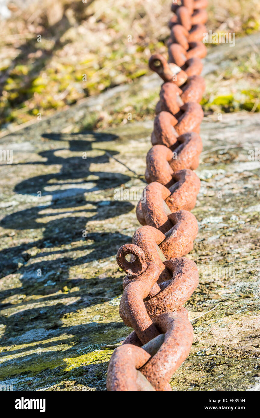 Old, big rusty iron chain on granite hill side. Sunlight creates fine ...