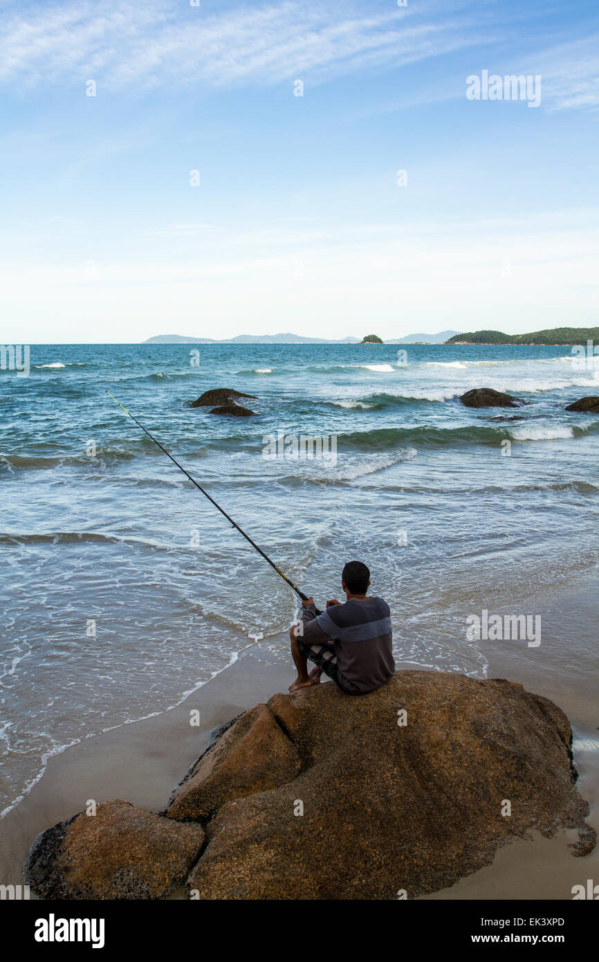 Man fishing sitting on a rock at Palmas Beach. Governador Celso Ramos ...
