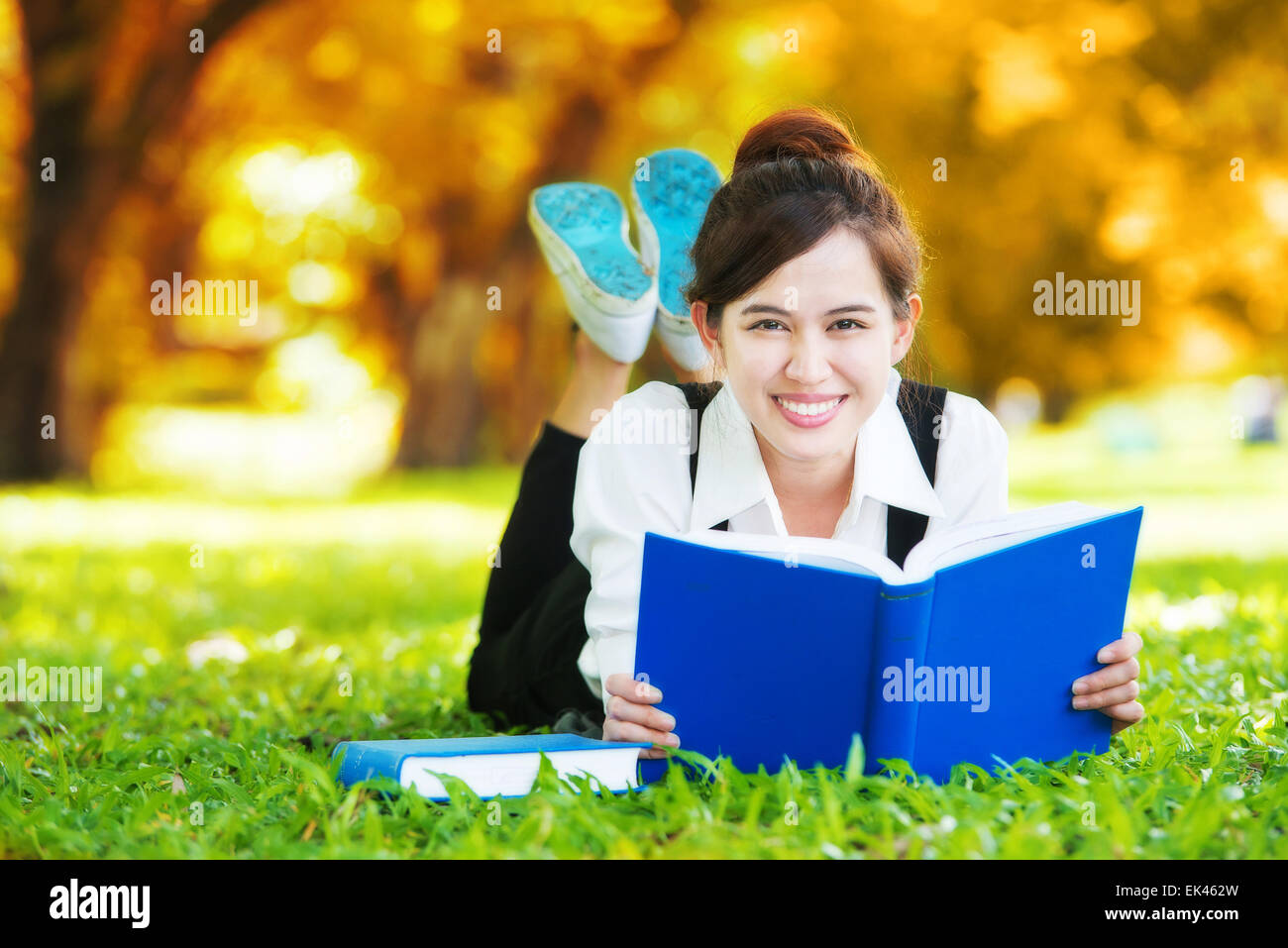Smiling casual student lying on grass reading book Stock Photo - Alamy