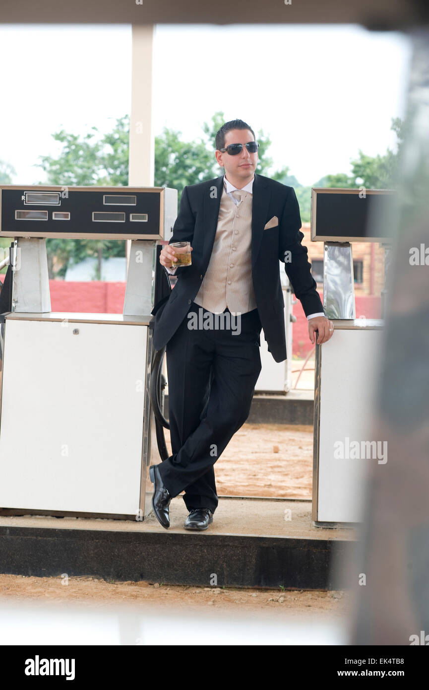 Handsome man in three piece suit at gas station drinking a whiskey ...