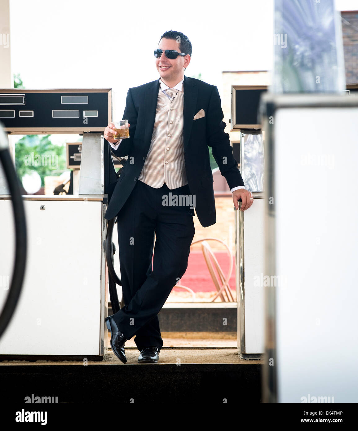 Handsome man in three piece suit at gas station drinking a whiskey ...