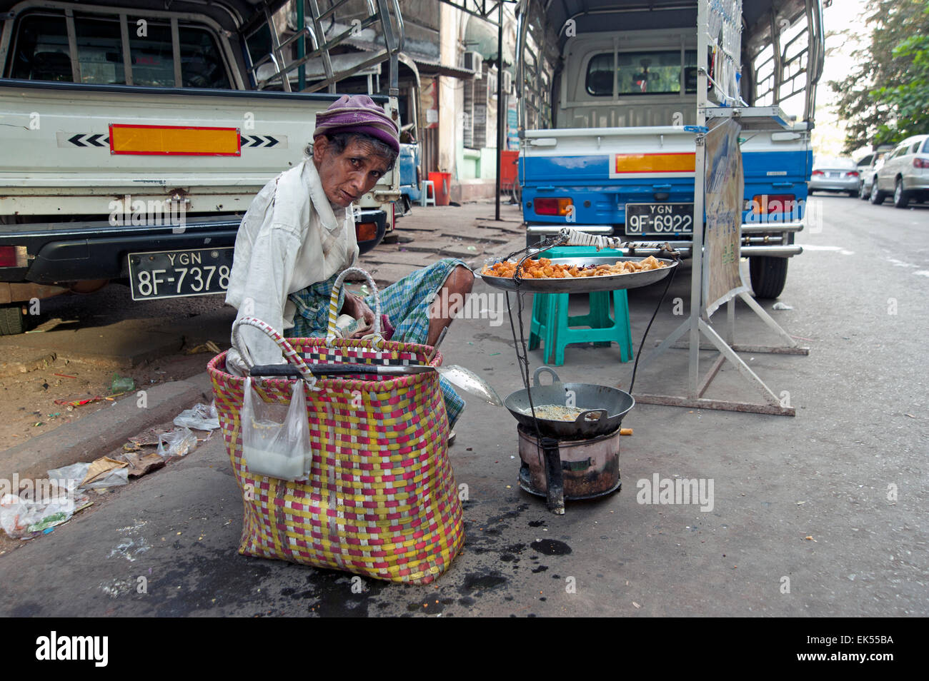 Old poor man dressing in rags sits by his mobile street kitchen fryer ...