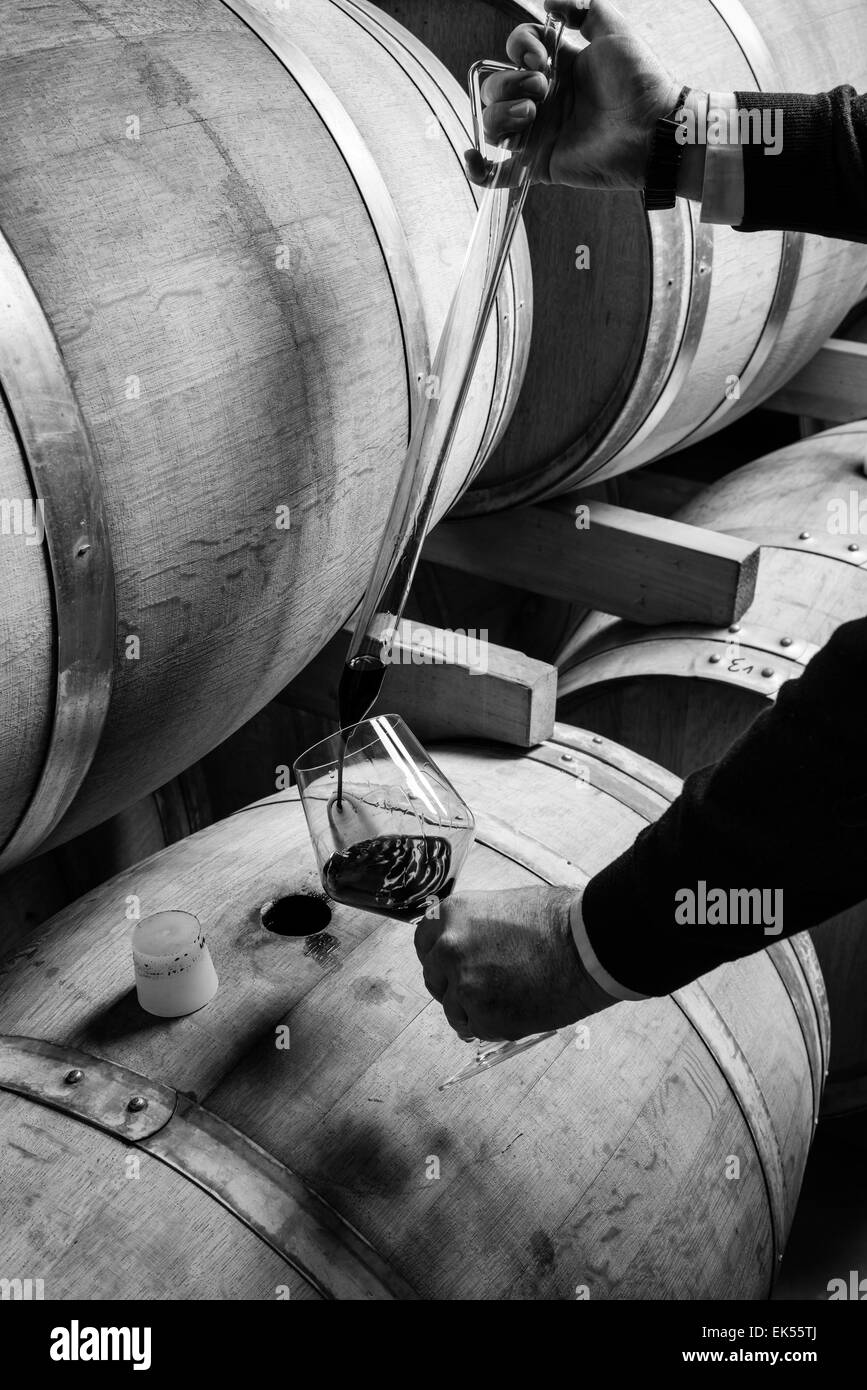 Italy, Sicily, red wine pouring from a wooden barrel into a glass in a ...